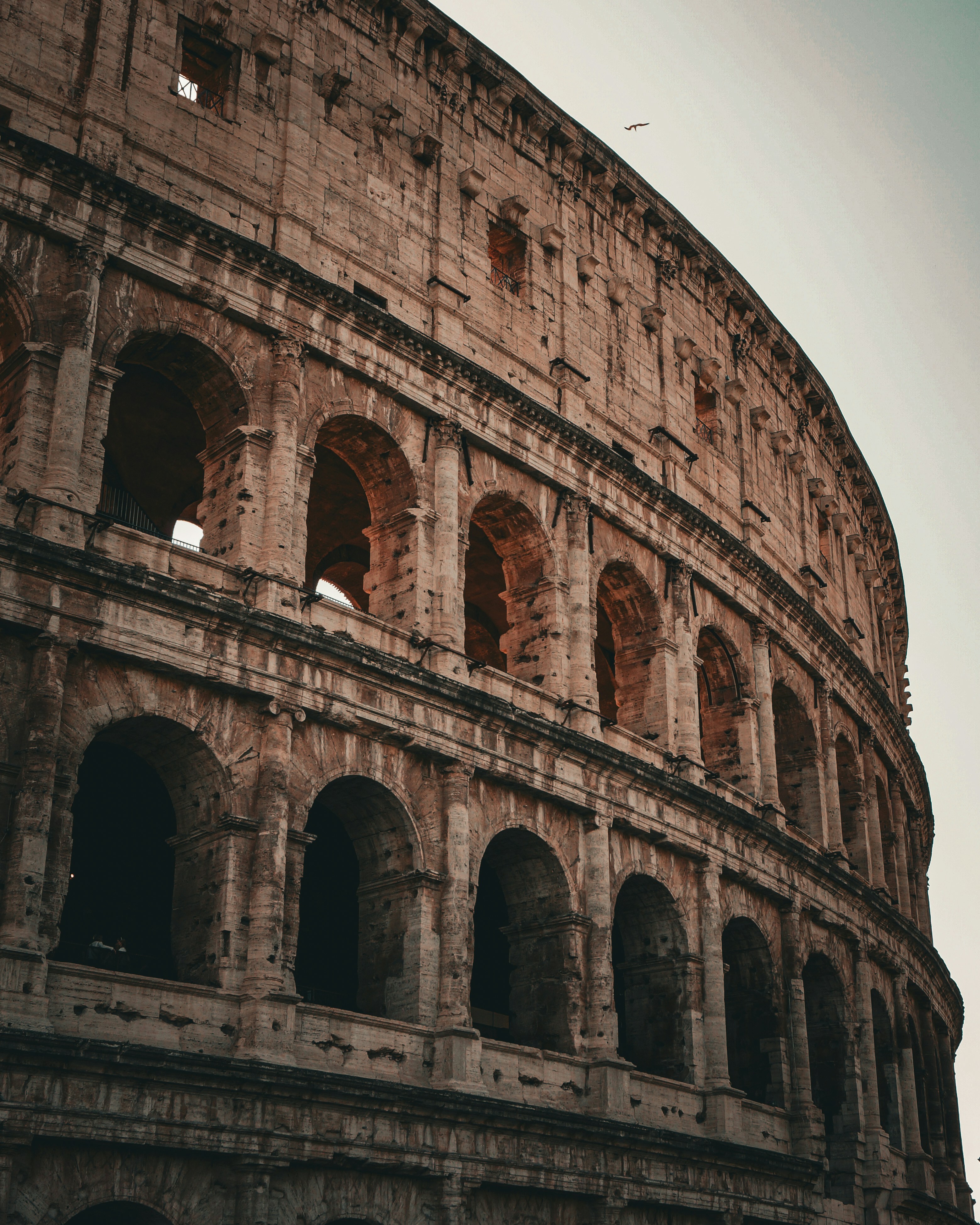 The Colosseum's weathered arches rise majestically against a pale sky, showcasing the grandeur of ancient Roman architecture.