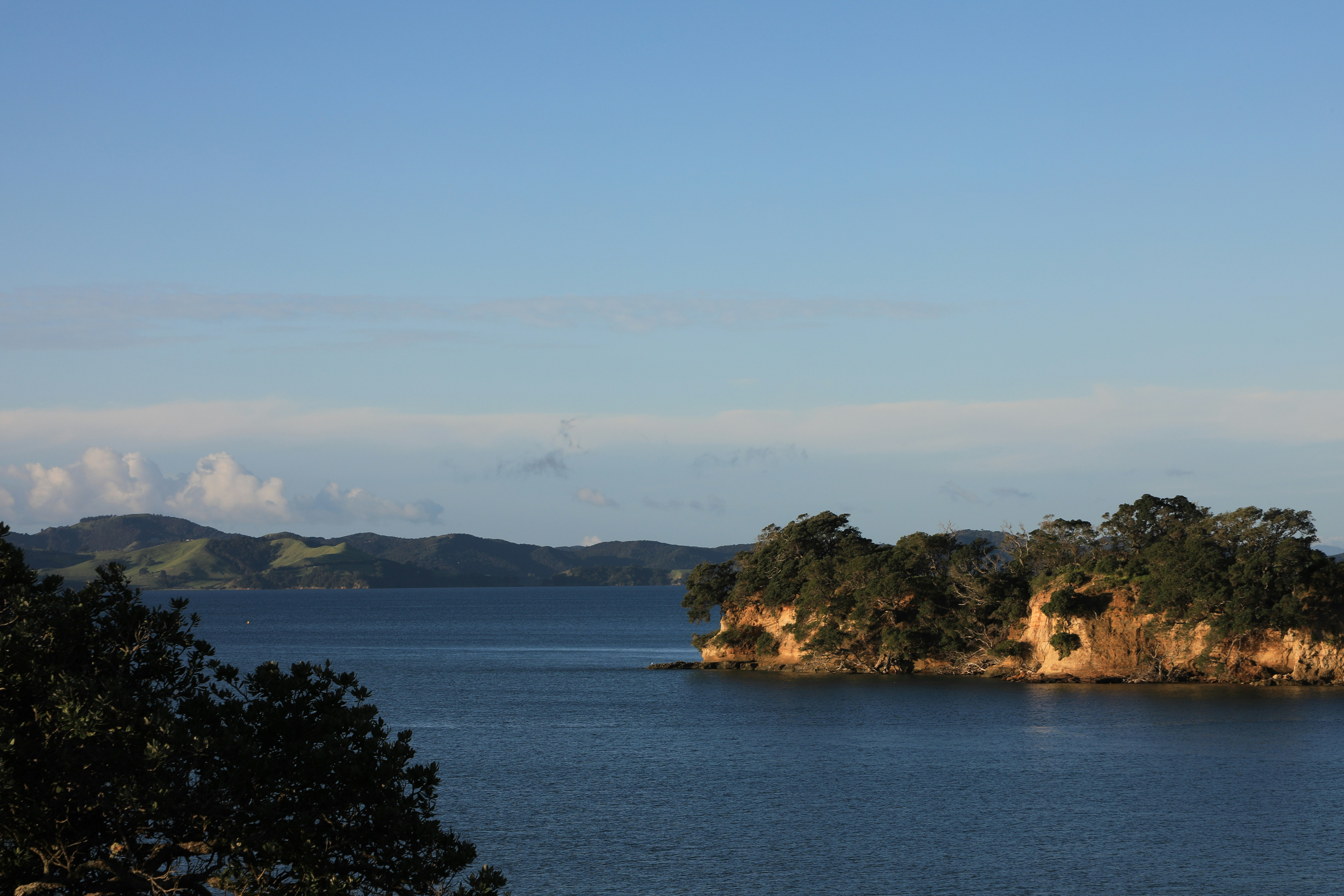 Tranquil coastal scene featuring a distant rocky outcrop surrounded by calm waters and lush greenery. Ideal for evoking a sense of peace.