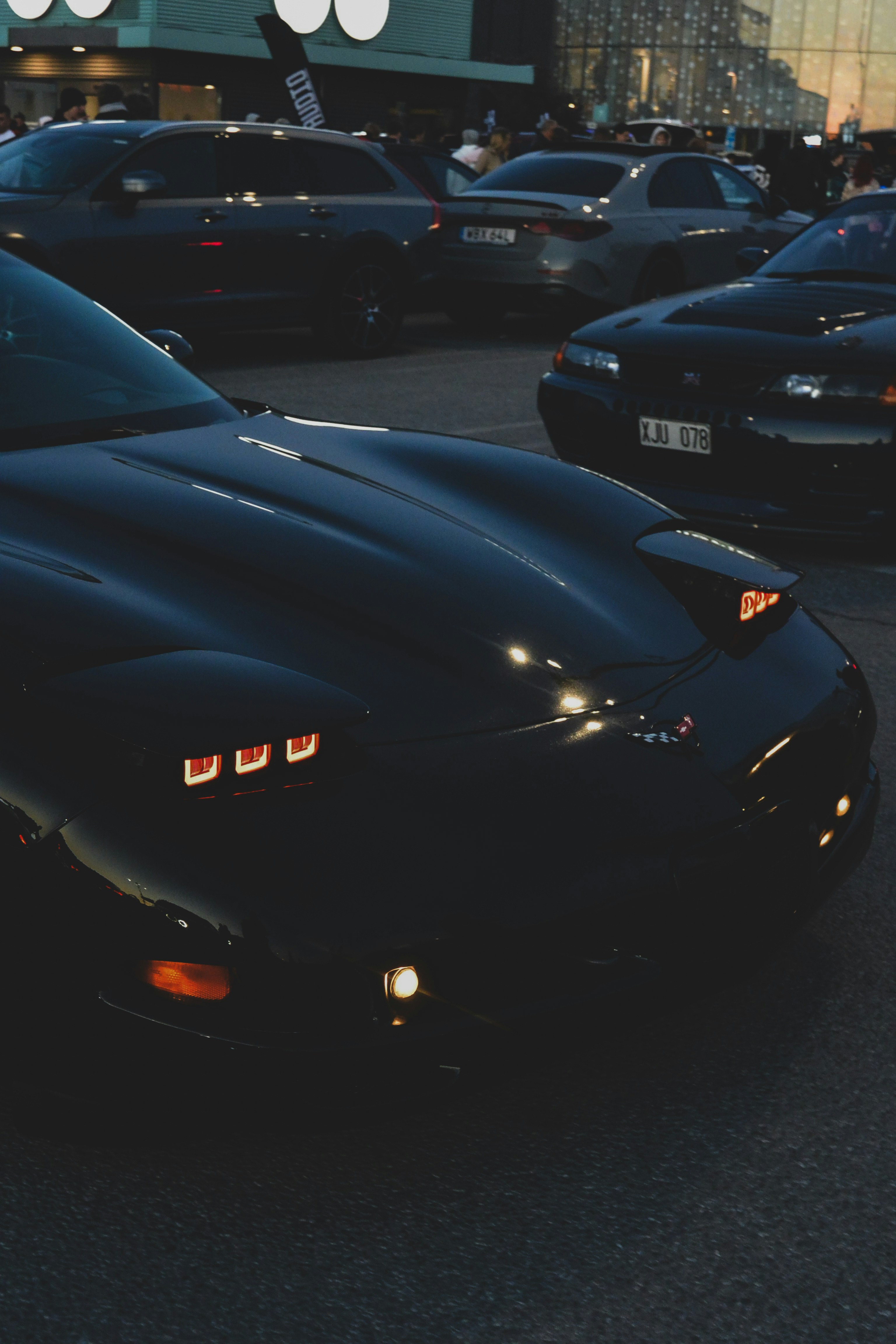 A sleek black sports car with distinctive headlights parked amidst a gathering of vehicles at dusk.