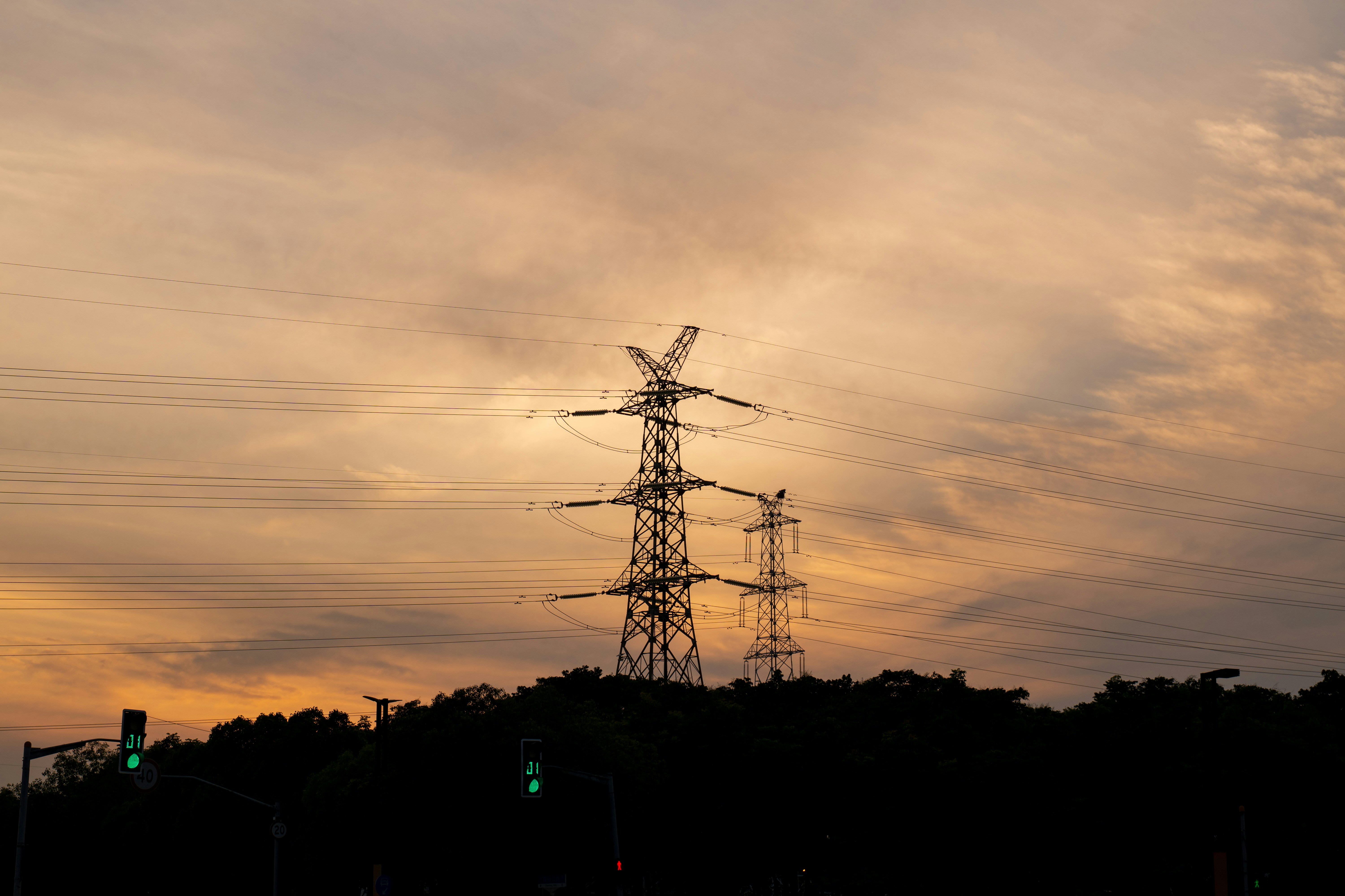 Silhouetted power lines and towers stand against a vibrant sunset, highlighting the contrast between nature and technology.