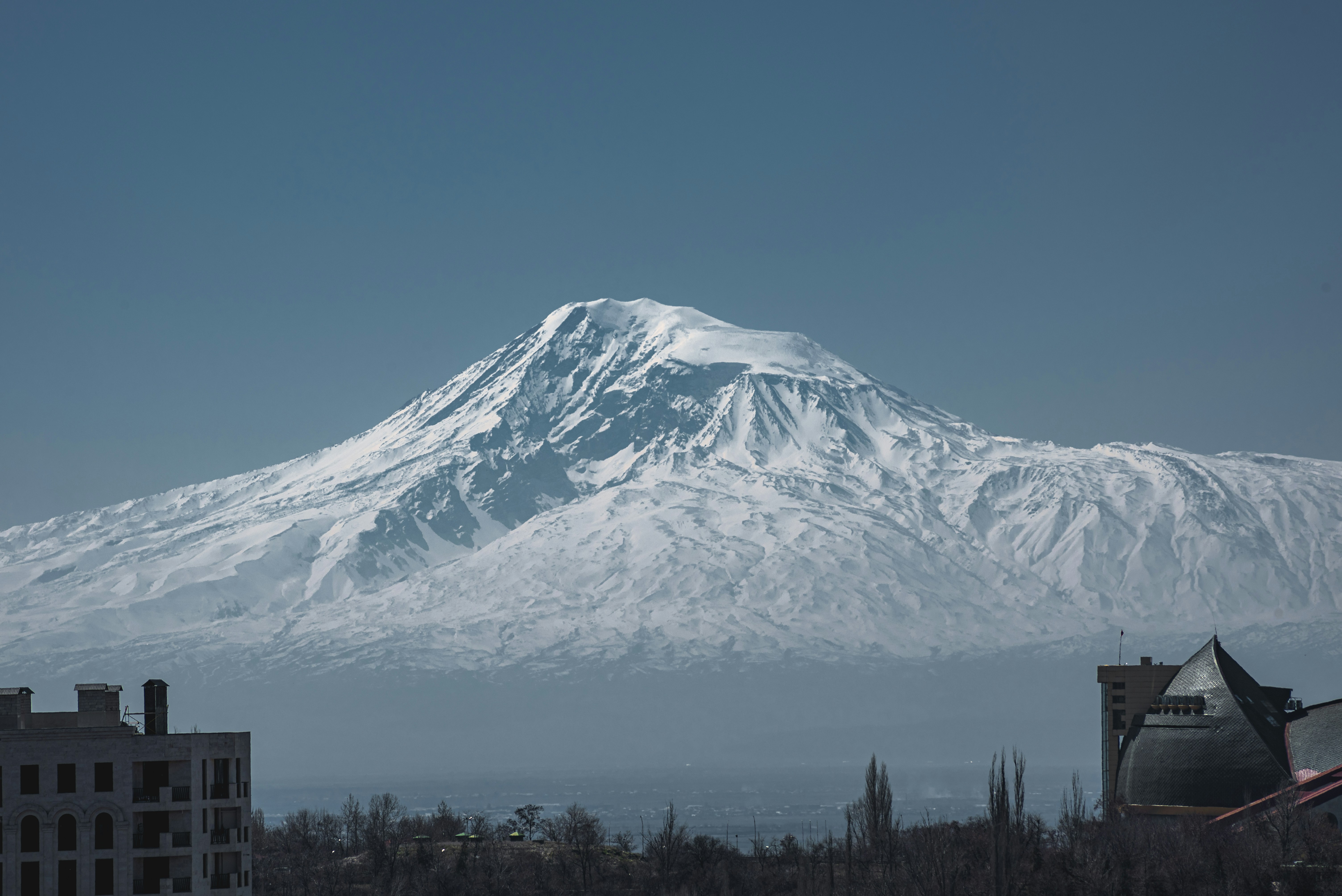 Snow-capped mountain peak rises majestically against a clear blue sky, dominating the landscape with its grandeur.