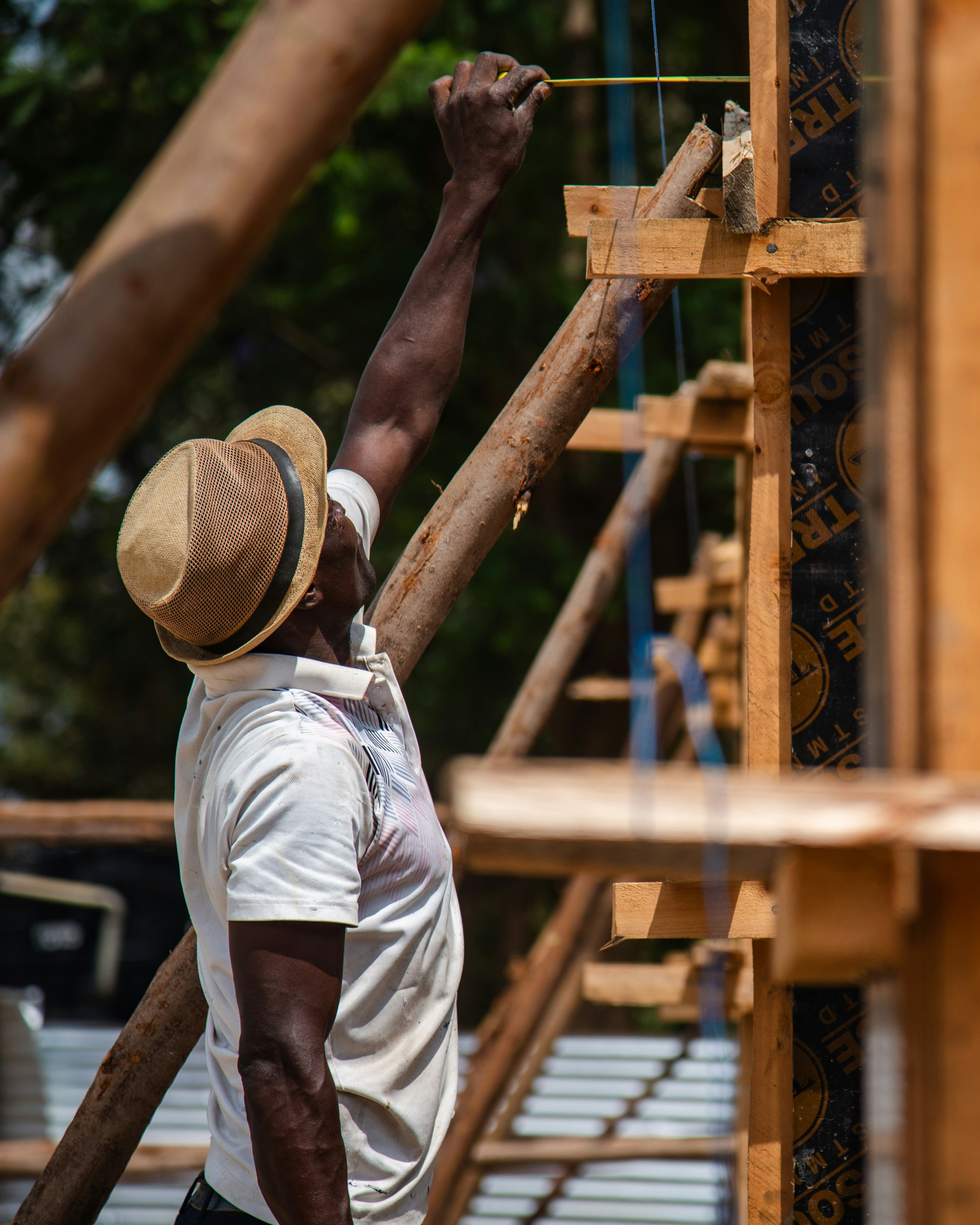 A worker measures a wooden beam on a construction site, showcasing the intricate details of craftsmanship and dedication.
