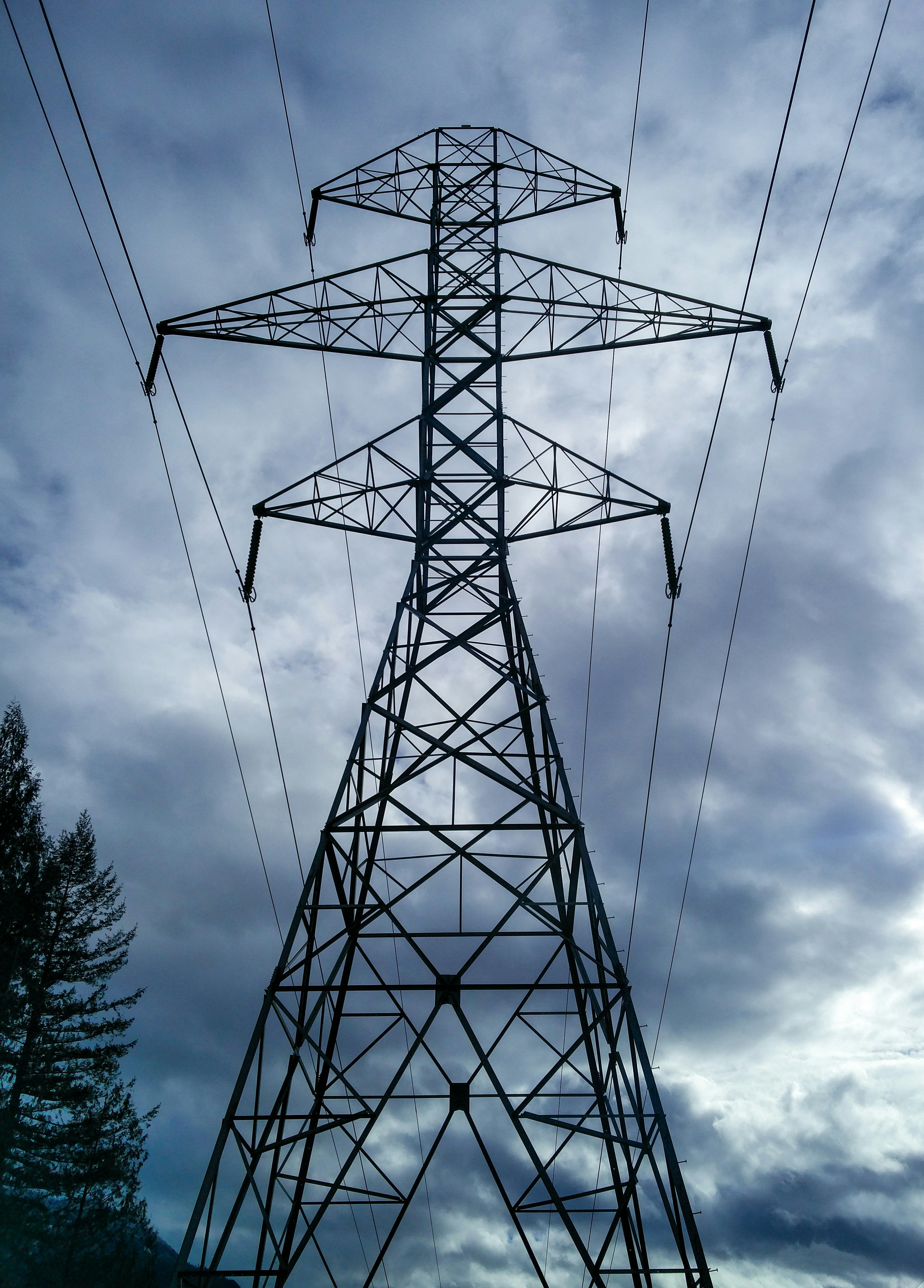 A tall power pylon stands against a cloudy sky.