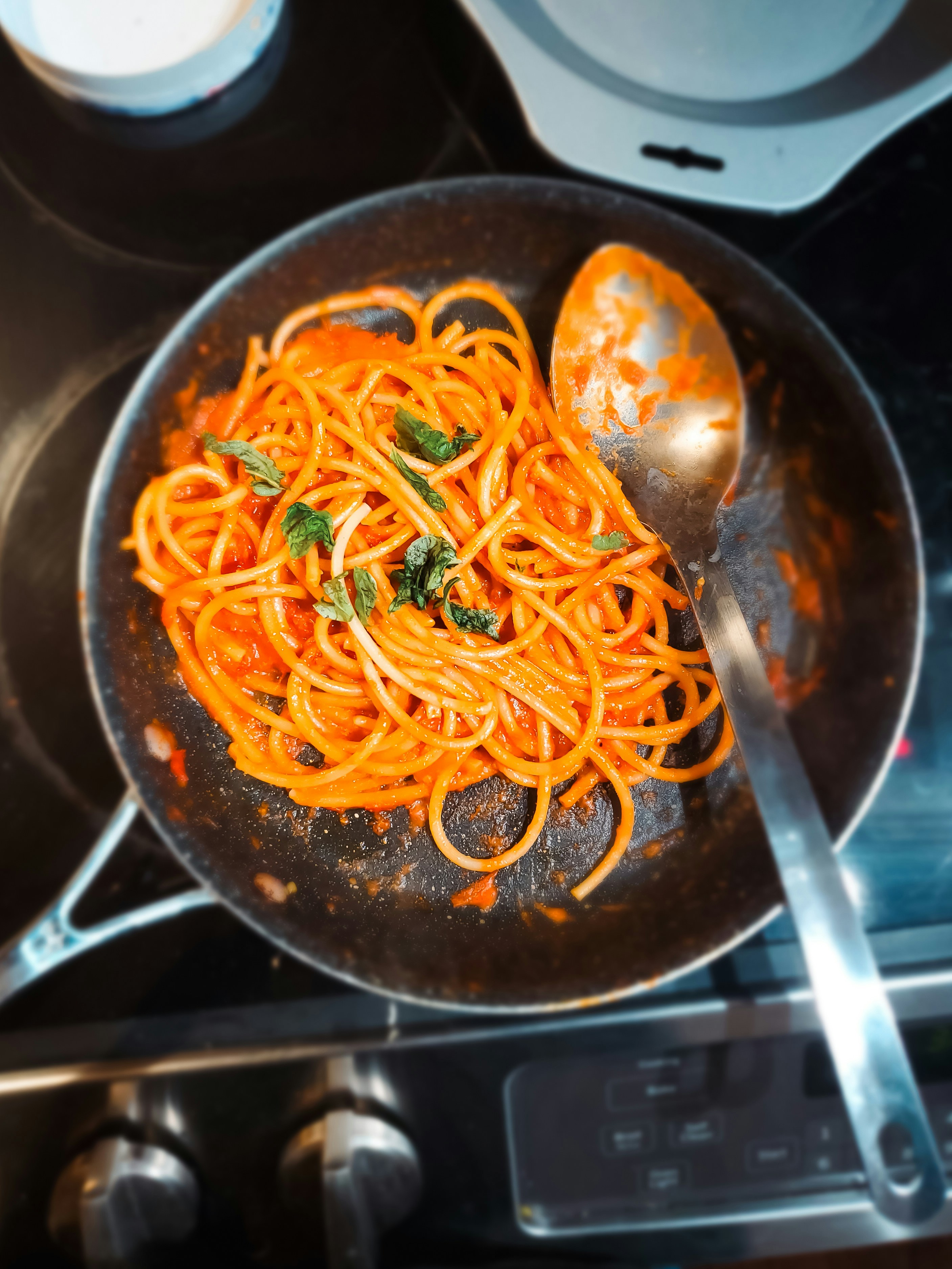 The image captures pasta being cooked in a pan with rich tomato sauce.