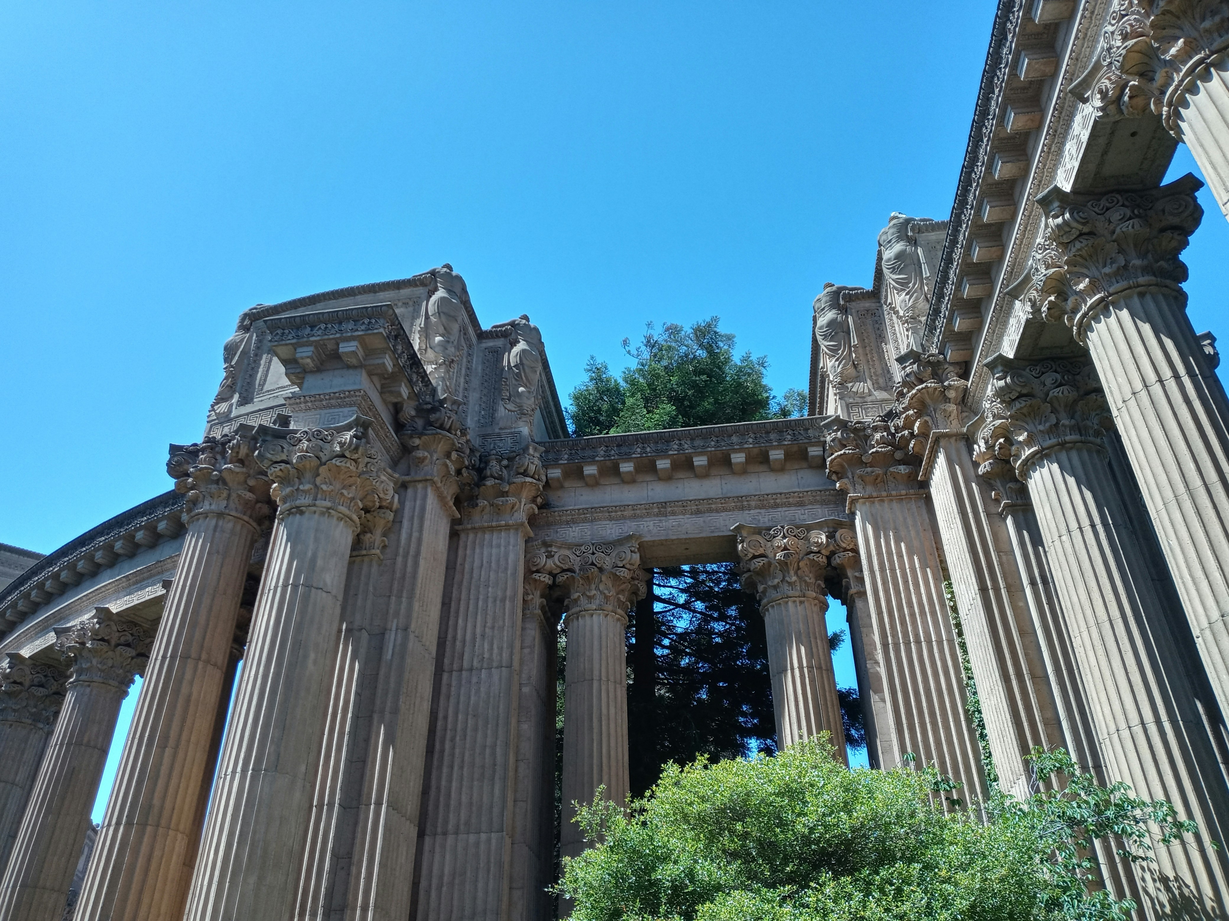 Majestic ruins of classical architecture framed by lush greenery under a clear blue sky.