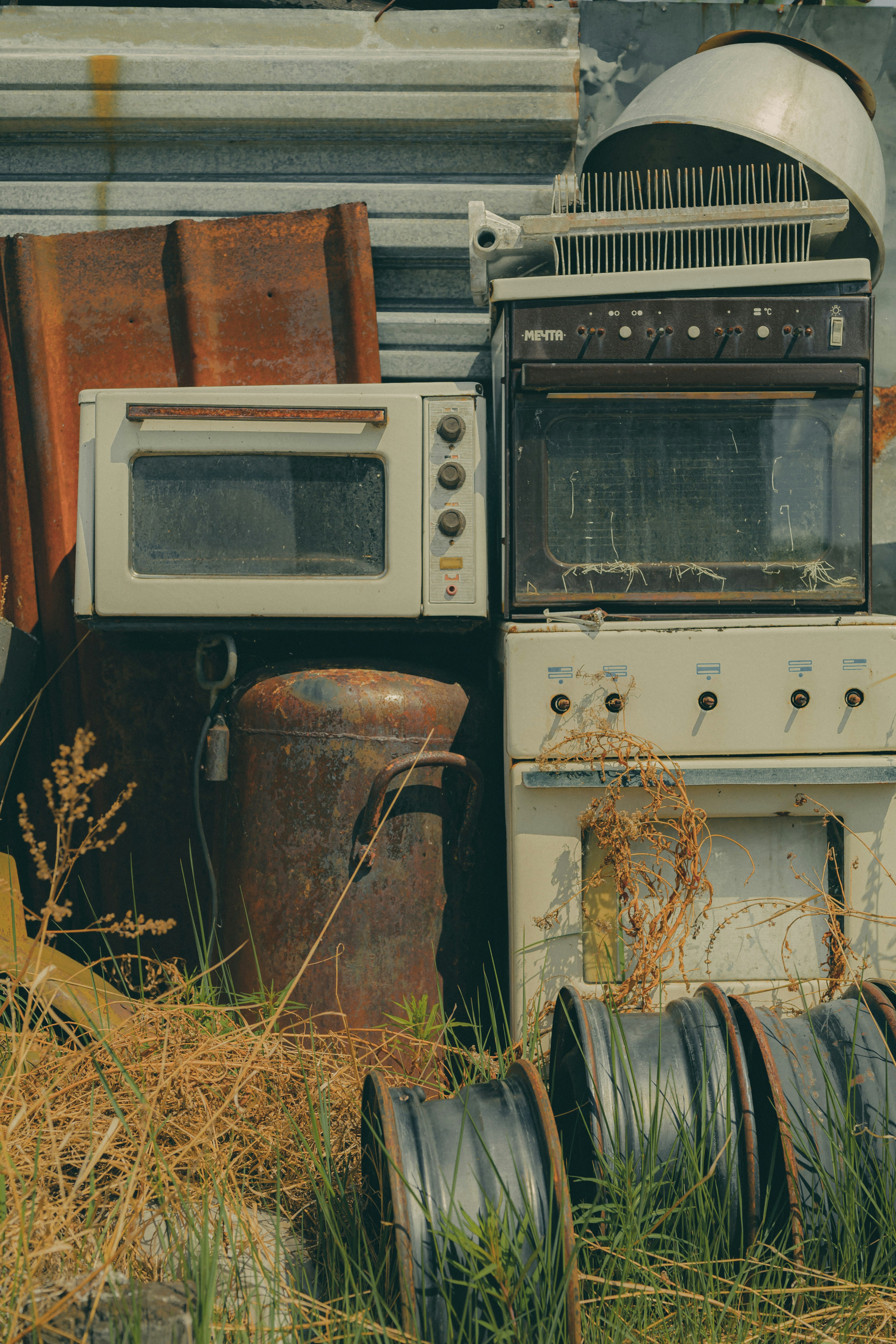 Still life of old and broken machinery and appliances against the wall of an old warehouse | Old appliances and other items sit discarded.
