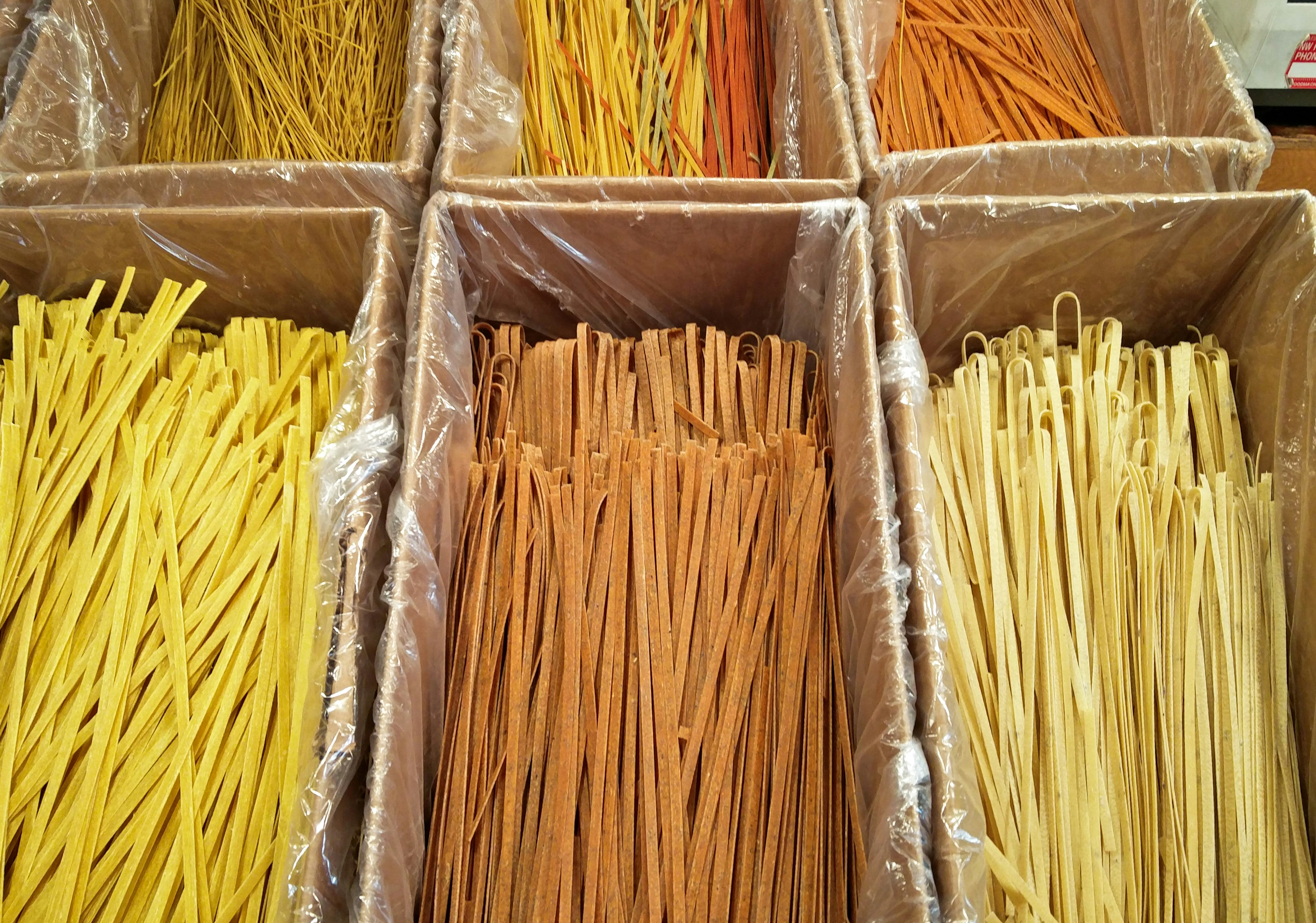 Vibrant assortment of pasta varieties displayed in wooden boxes, showcasing shades of yellow, orange, and brown.