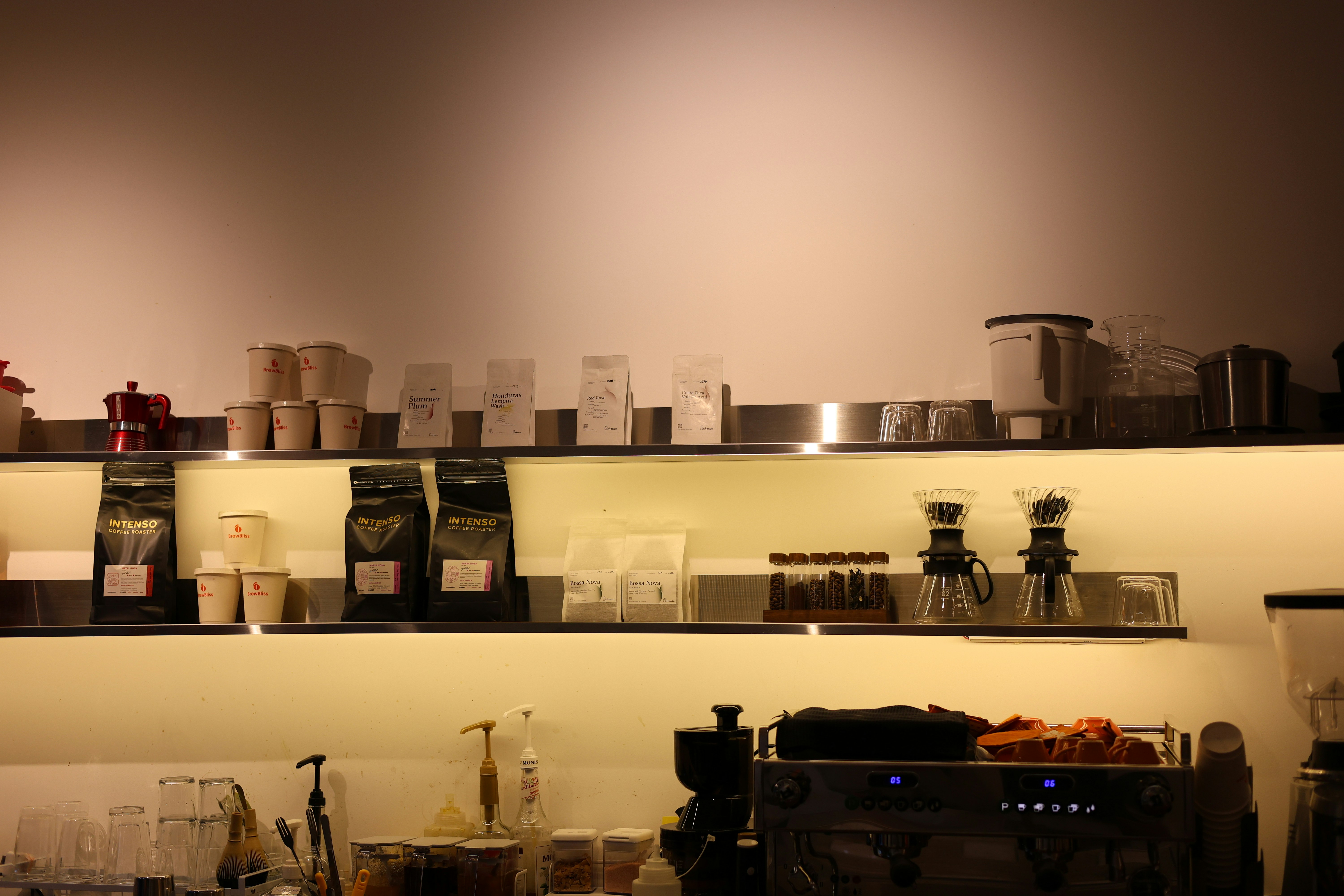 Coffee shop shelf displaying various containers and brewing tools, illuminated by soft ambient light.