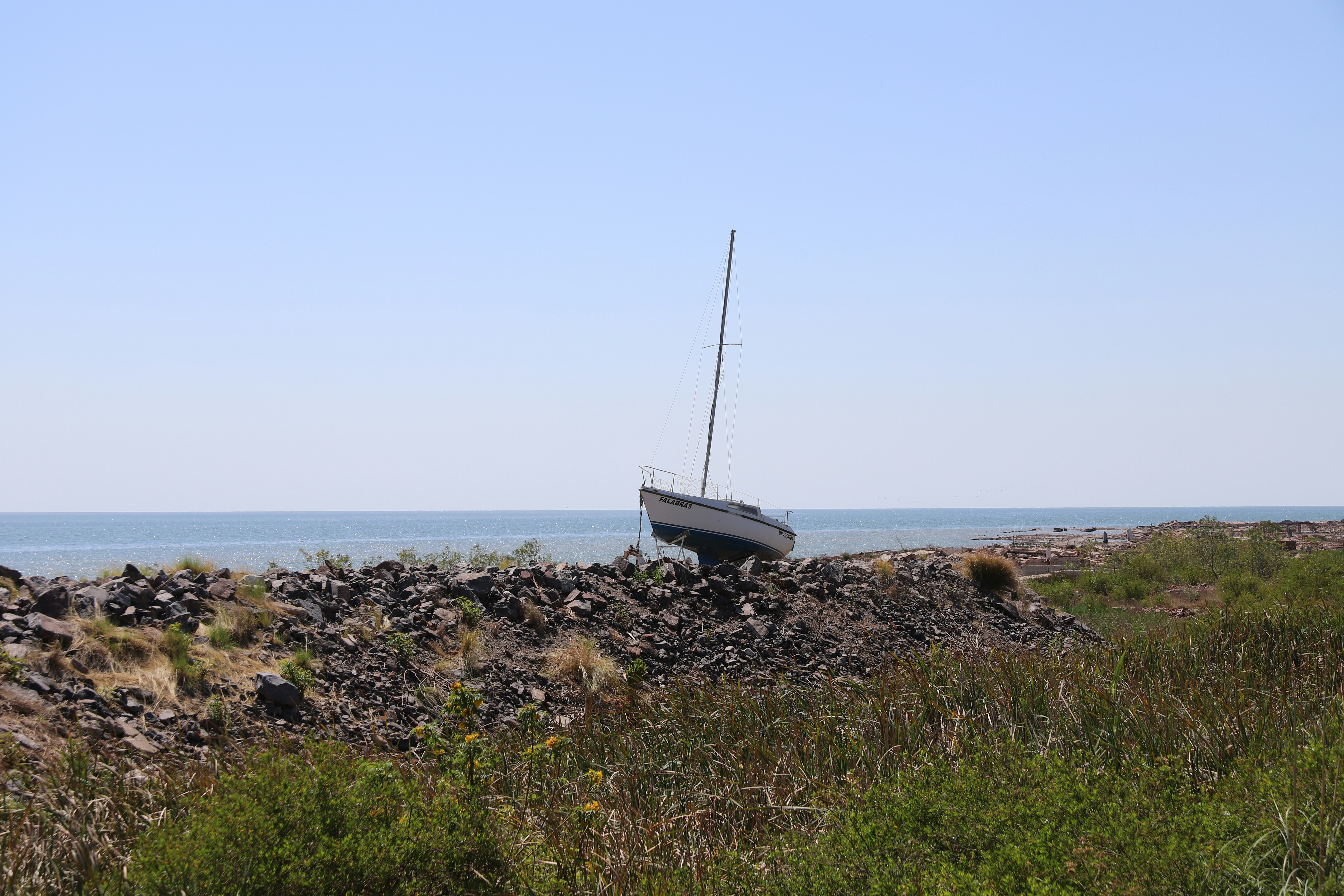 Lone Sailboat on a Rocky Shore Beneath a Quiet Horizon