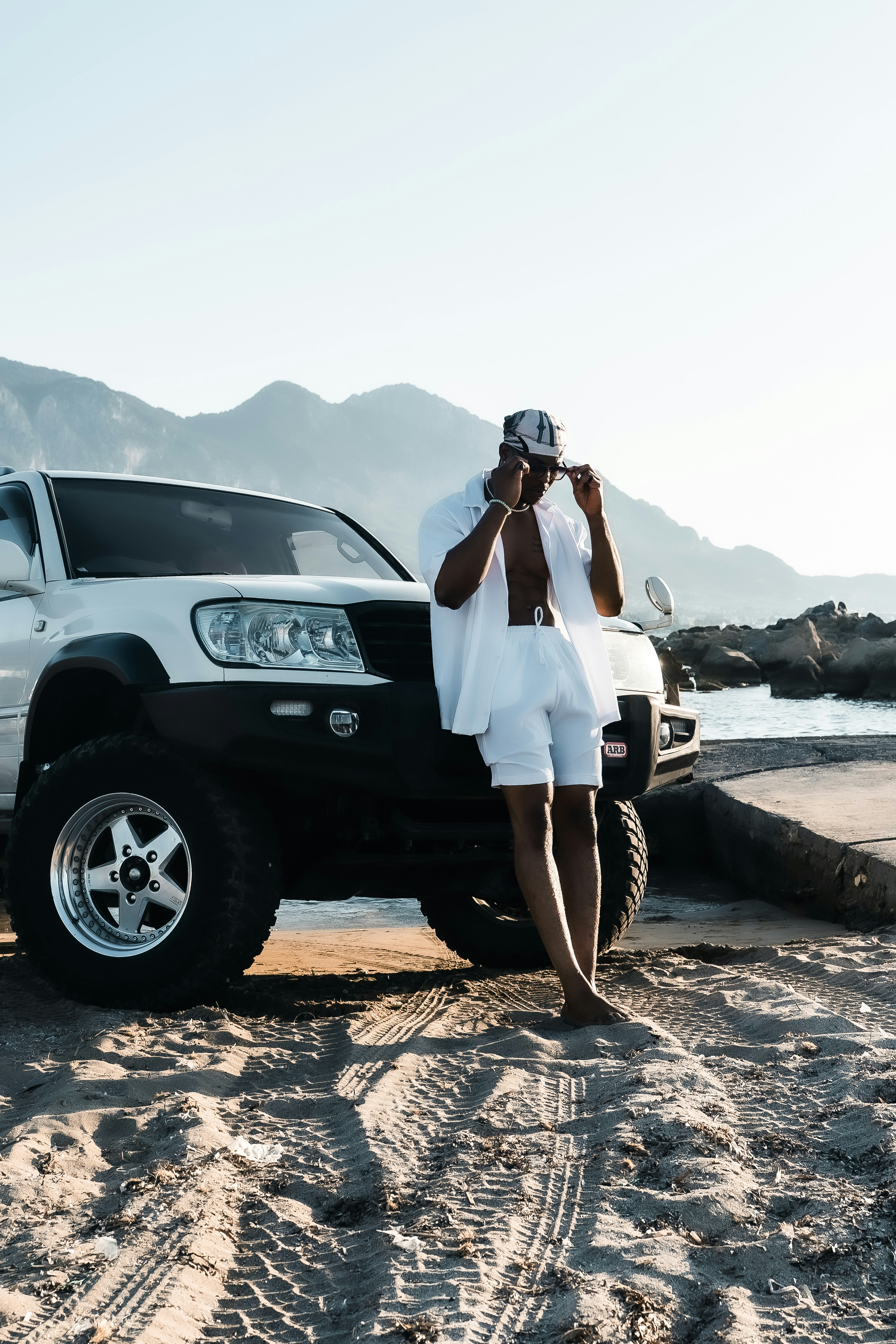 White-sand confidence: a stylish figure by the rugged sea and SUV
