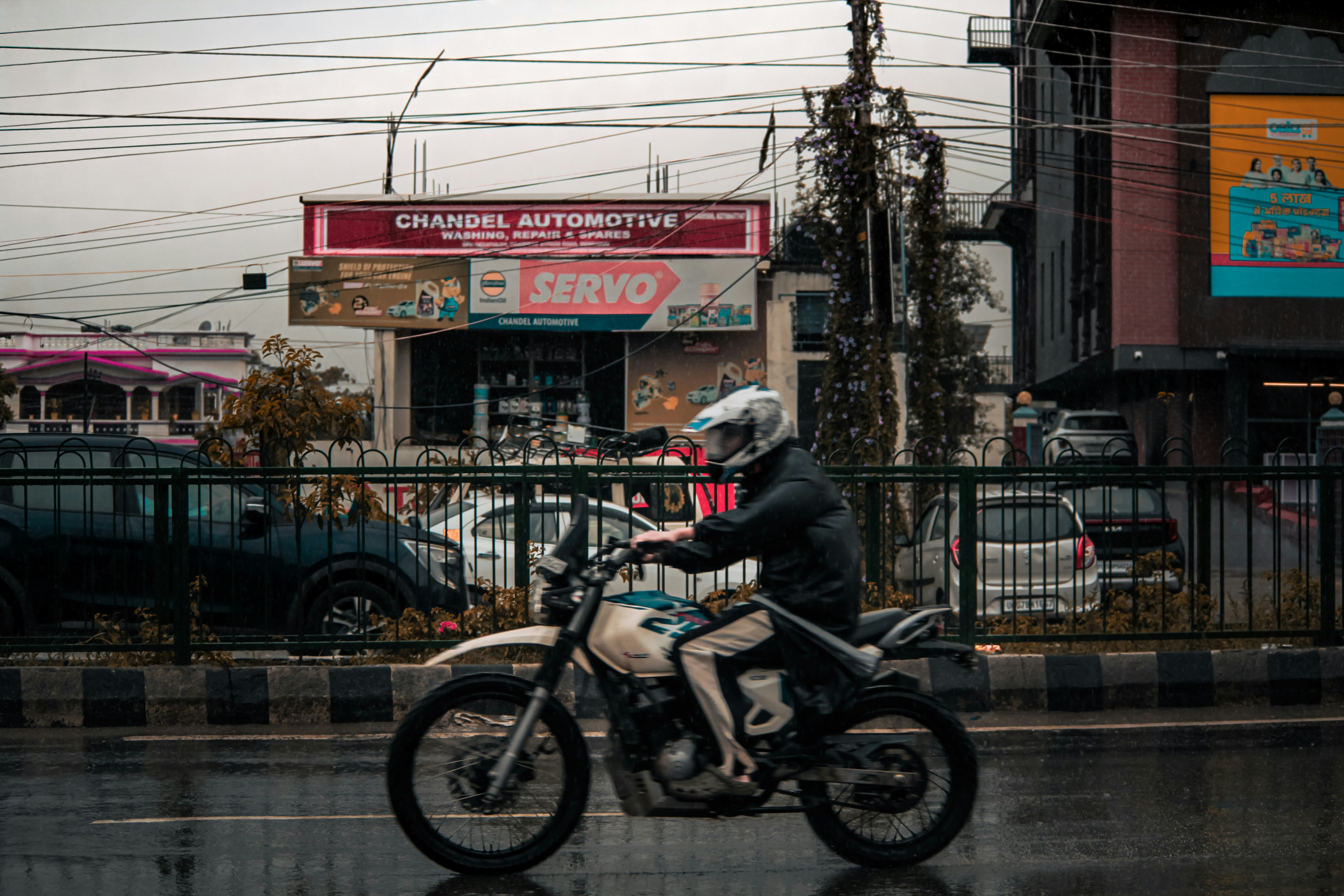 A motorcycle speeds past a busy automotive shop on a rainy day, capturing the essence of urban life in motion.