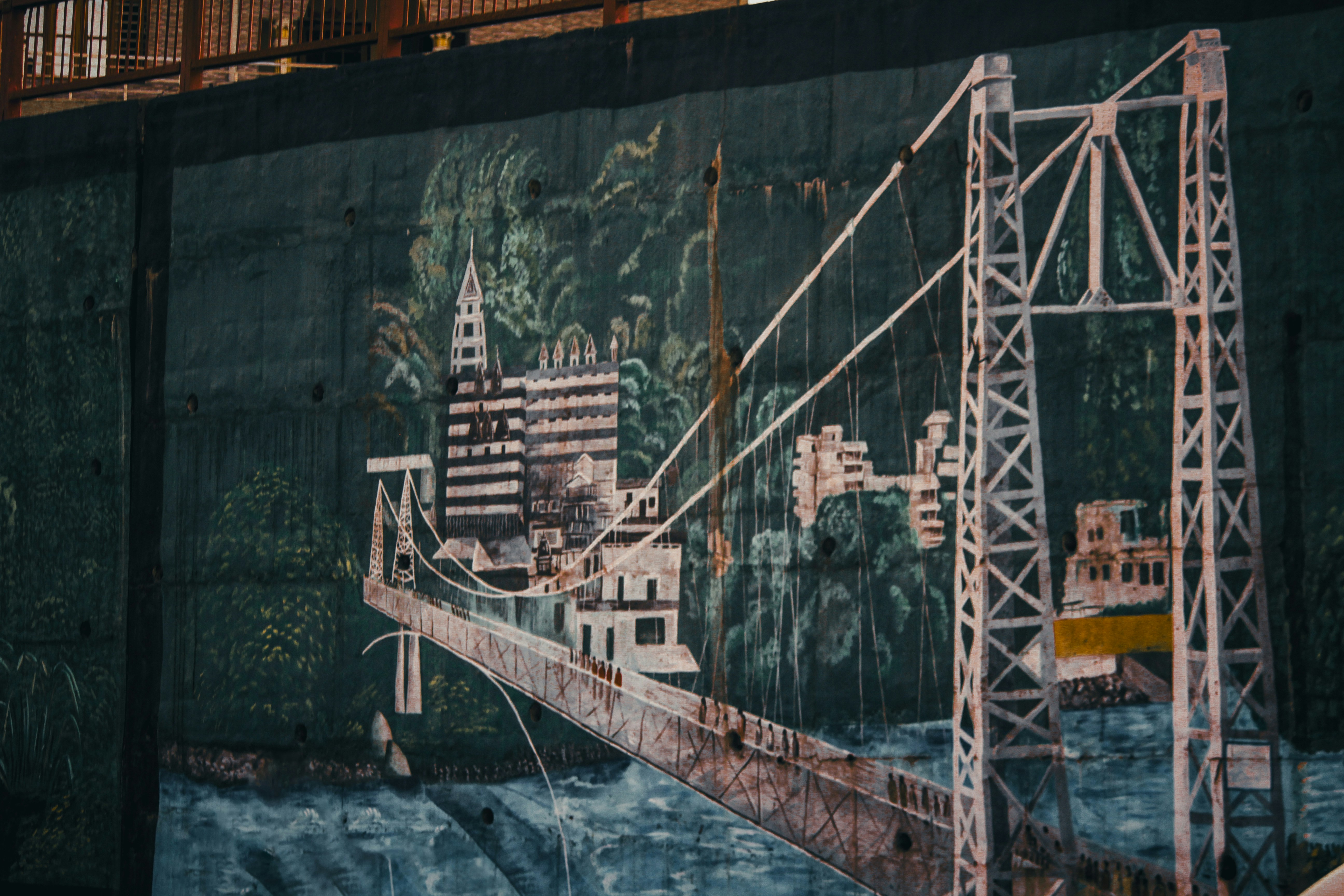 A vibrant mural depicting a bridge alongside a cityscape, showcasing intricate details of architecture and nature. The artwork reflects the harmony between urban structures and the surrounding environment.