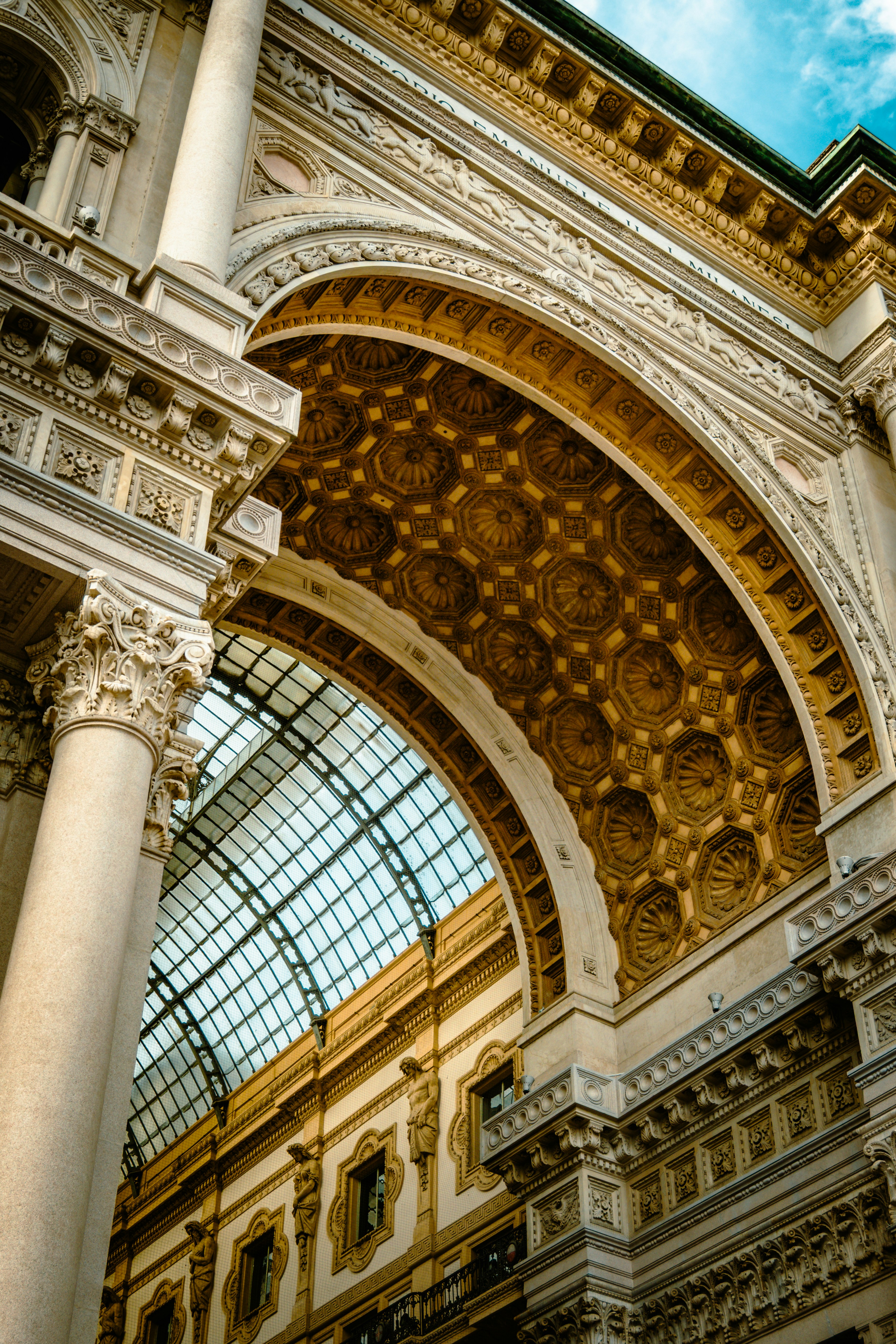 Intricate ceiling details and grand columns frame a glass-roofed atrium, showcasing the harmony of classical design and modern architecture.