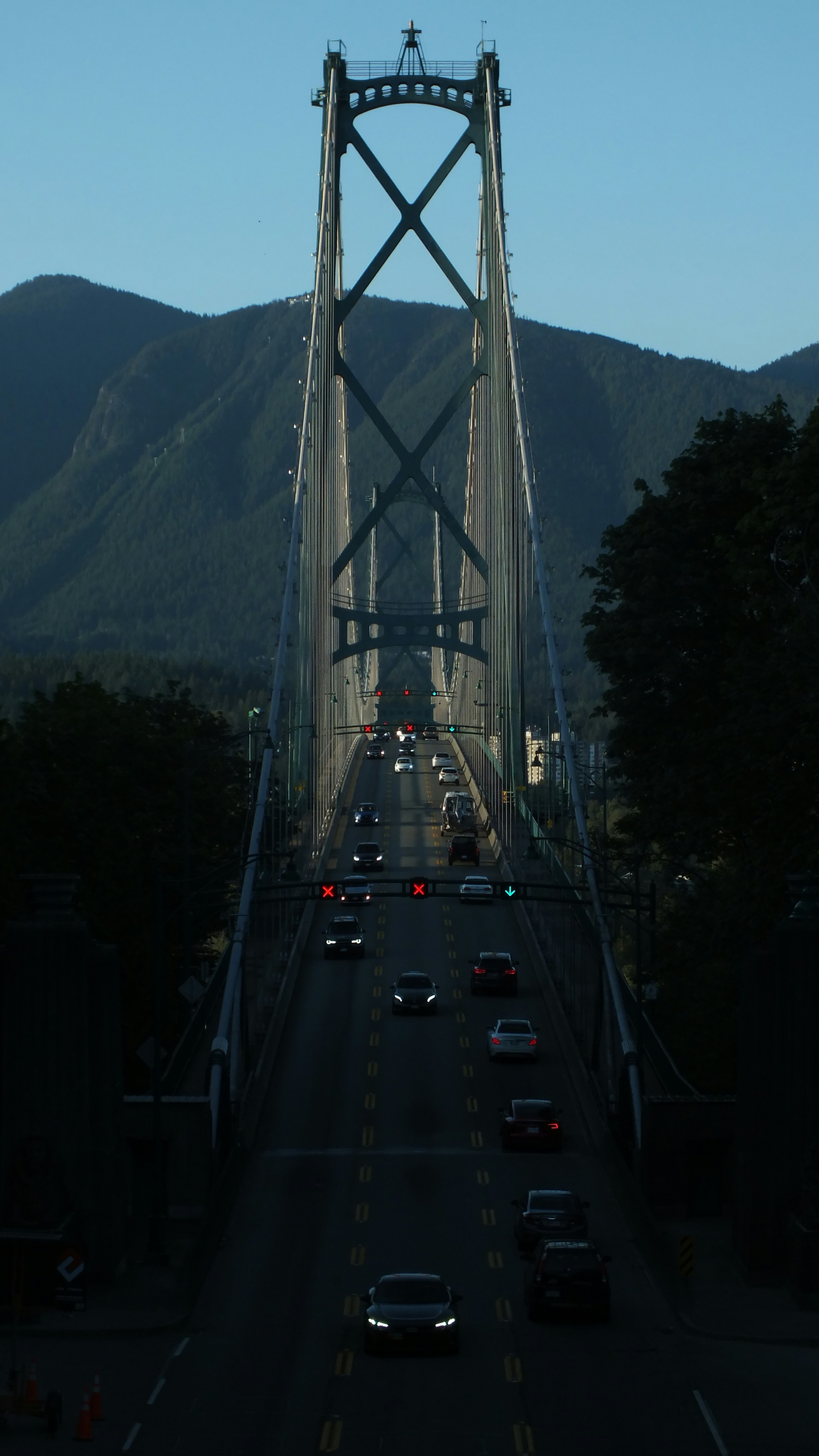 Suspension bridge spanning a valley, framed by mountains, with vehicles traversing the roadway beneath a twilight sky.