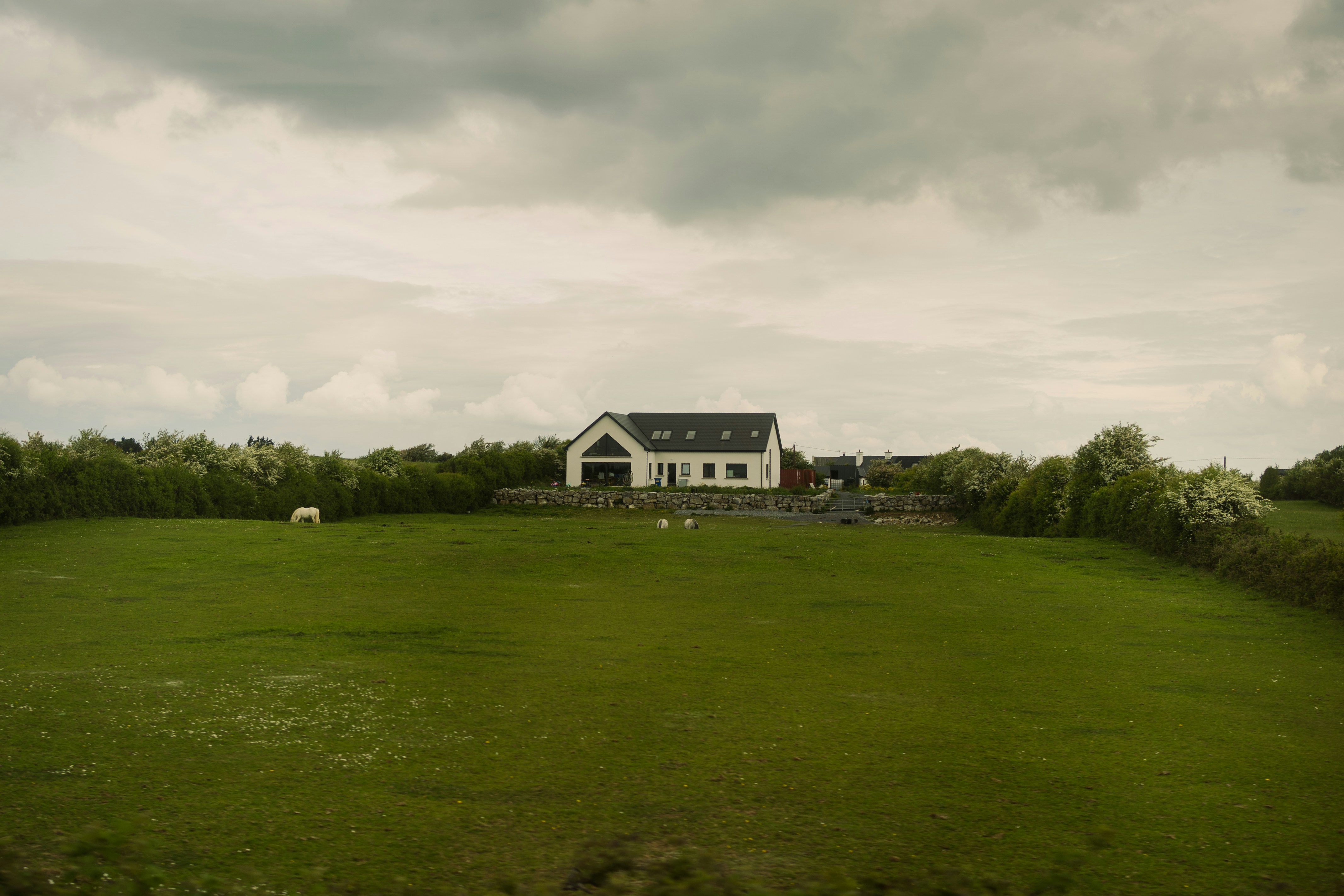A modern house set against a backdrop of lush green fields and cloudy skies, embodying tranquility in rural life.