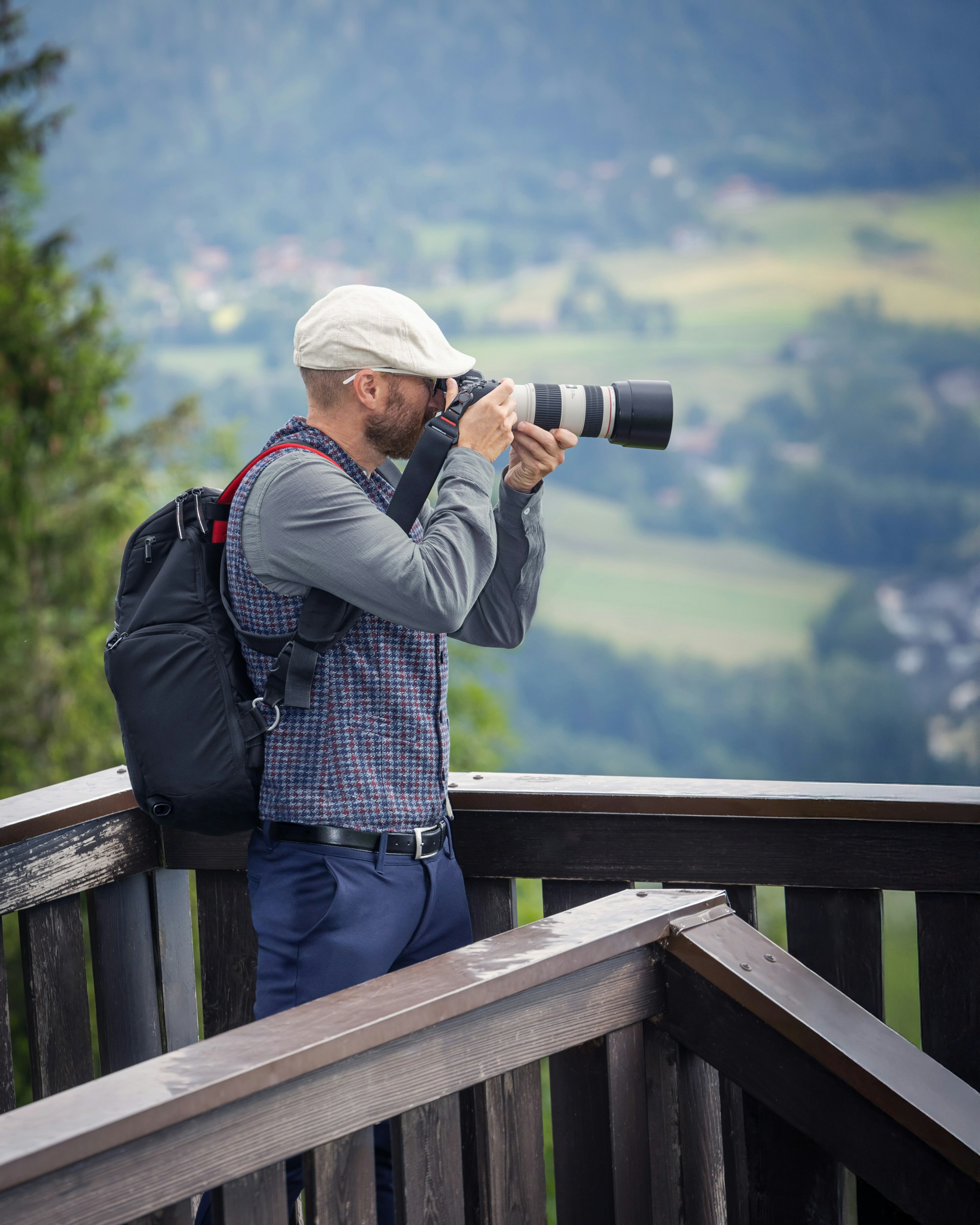 A photographer poised on a wooden platform, focusing intently on the expansive landscape with a telephoto lens. The scene showcases the blend of human creativity and natural beauty.