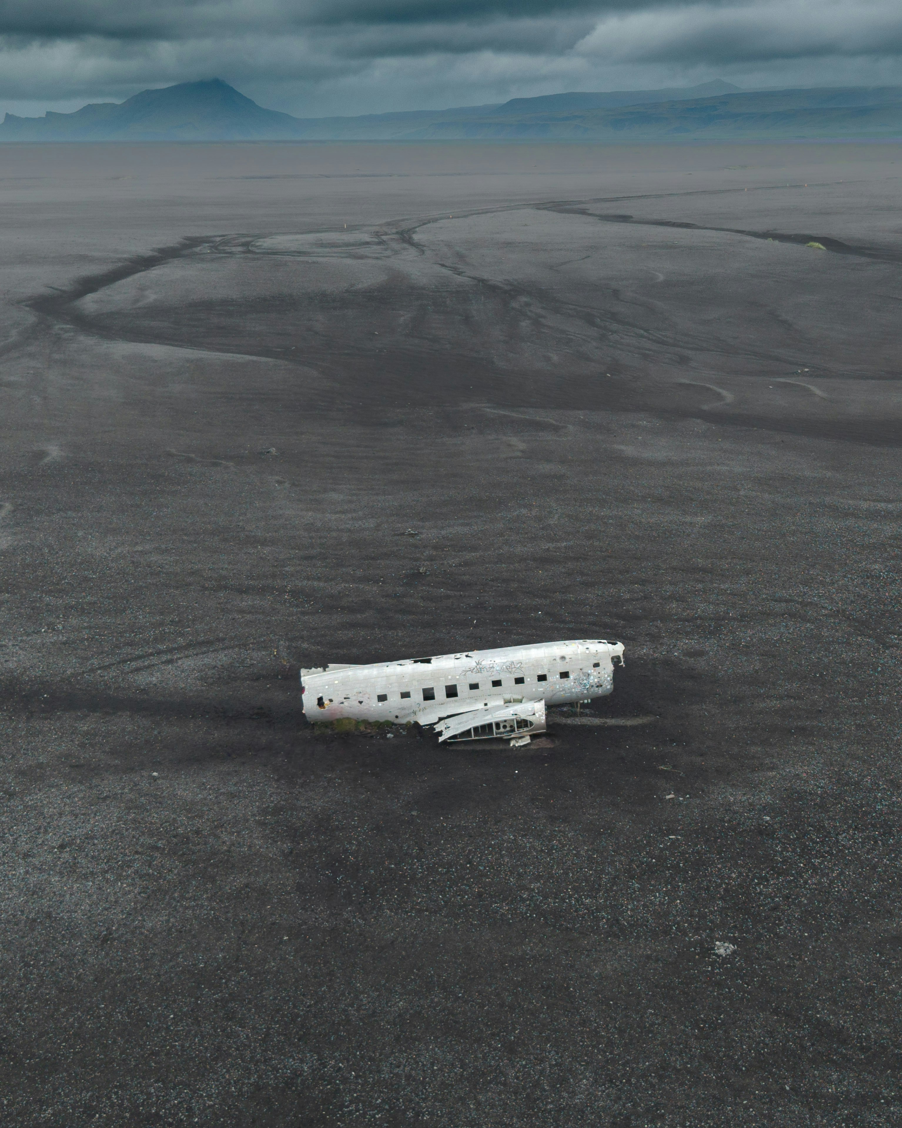 A moody DC3 plane wreck sits stranded on the vast black sand of Sólheimasandur Beach in Iceland, evoking a sense of adventure and solitude. | Wrecked airplane in a barren, moody landscape.