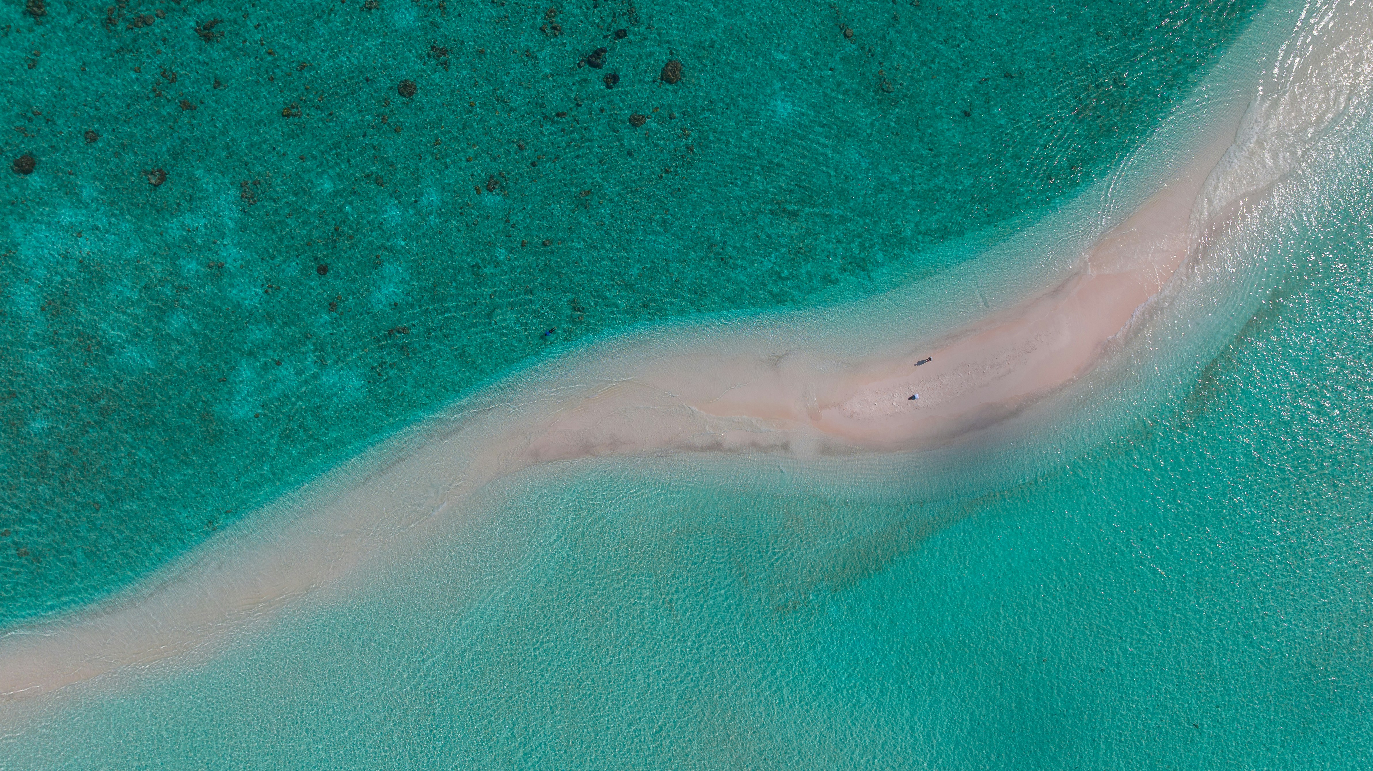 Aerial view of a sandy shoal winding through vibrant turquoise waters, showcasing the interplay of land and sea.