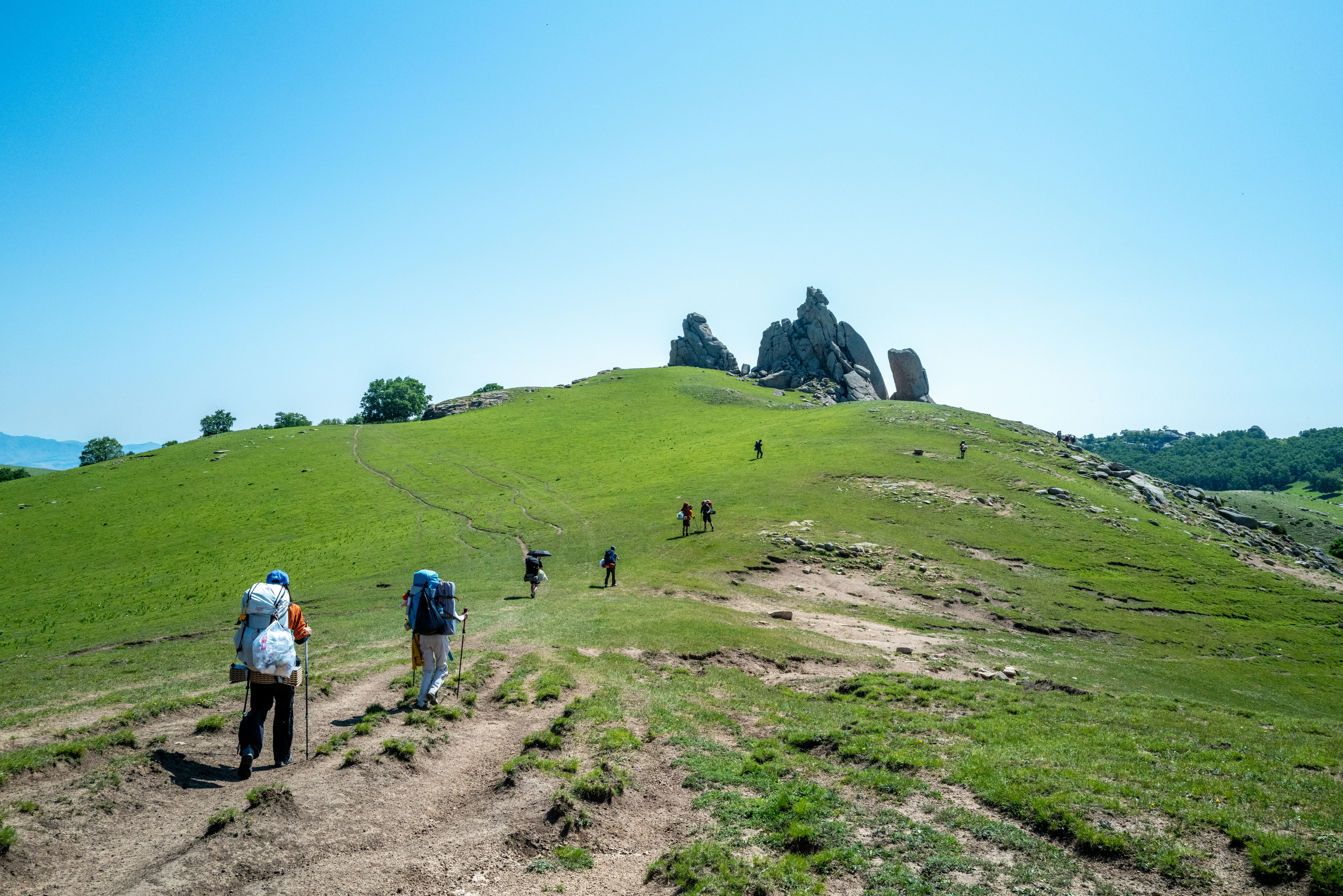 Hikers Ascend the Lime-green Ridge Toward the Rock Monolith