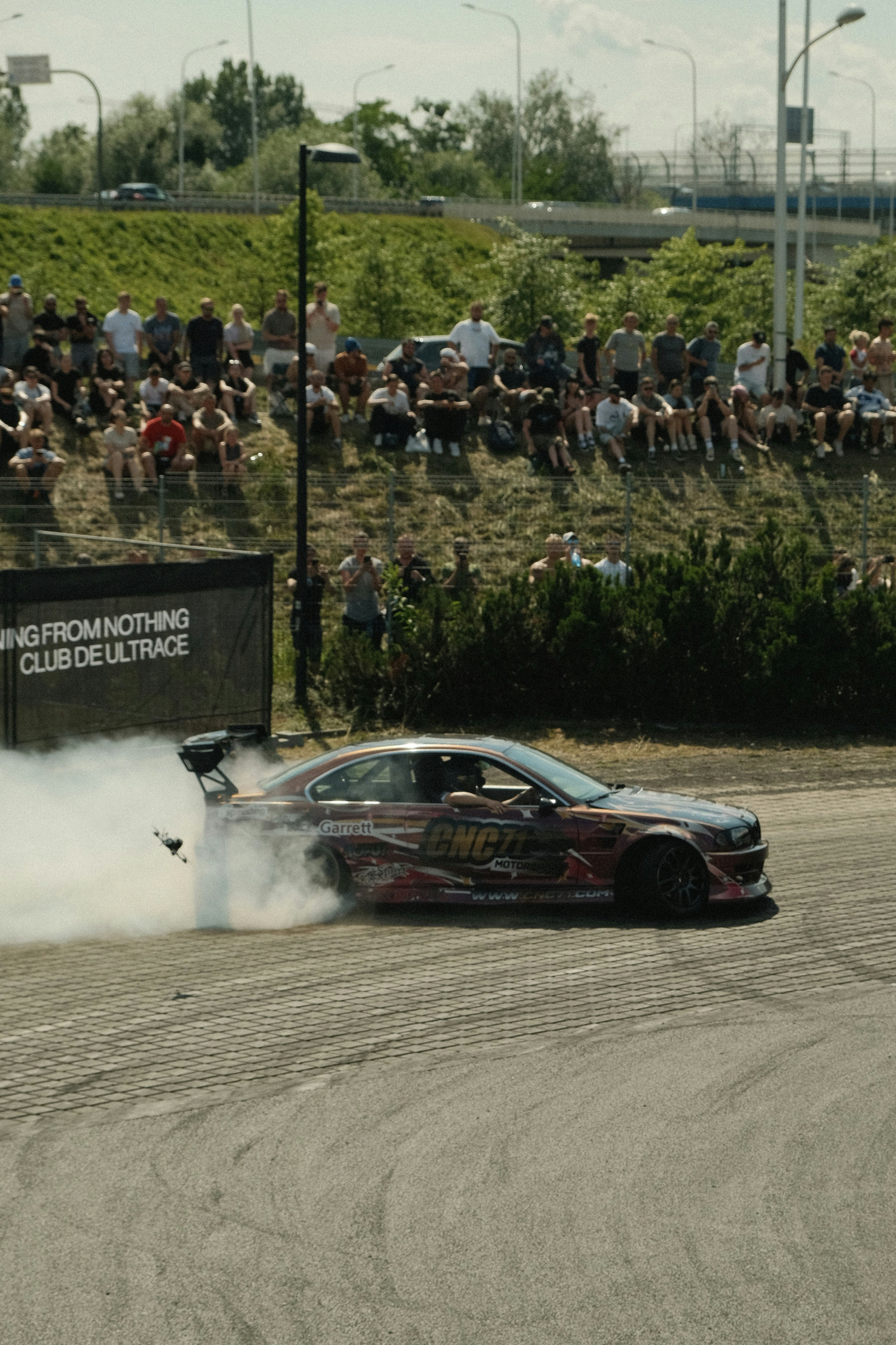 Red Drift Through Smoke: A race car powers a plume past a packed hillside crowd.