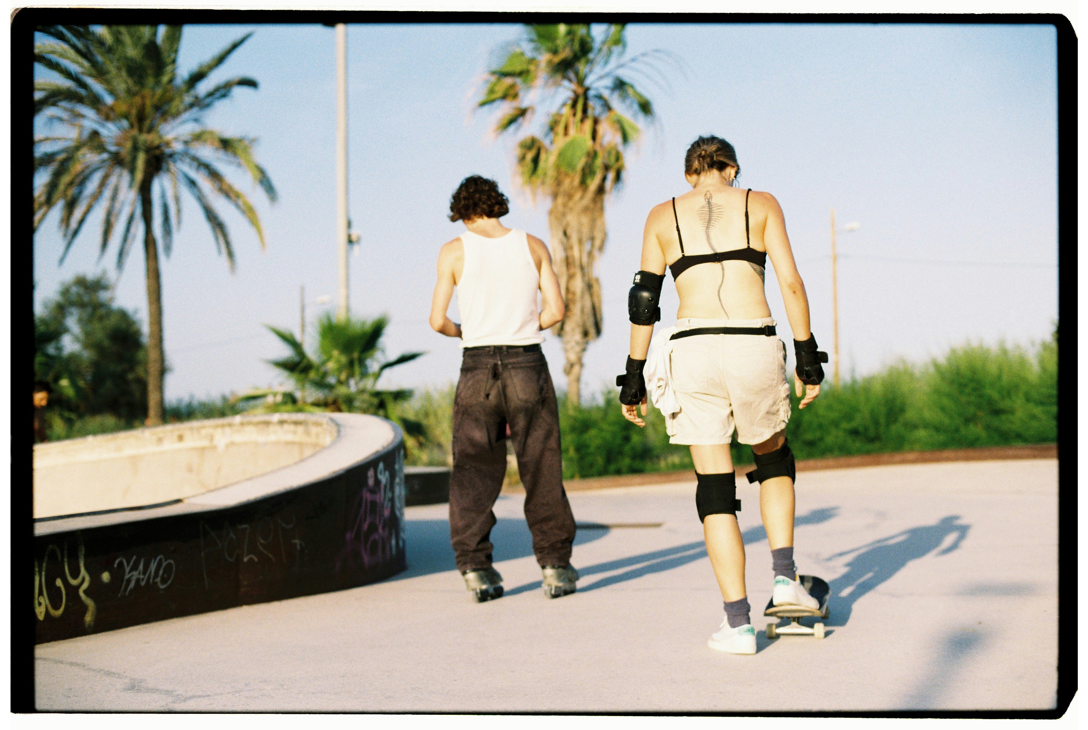 Two people are at a skatepark on a sunny day.