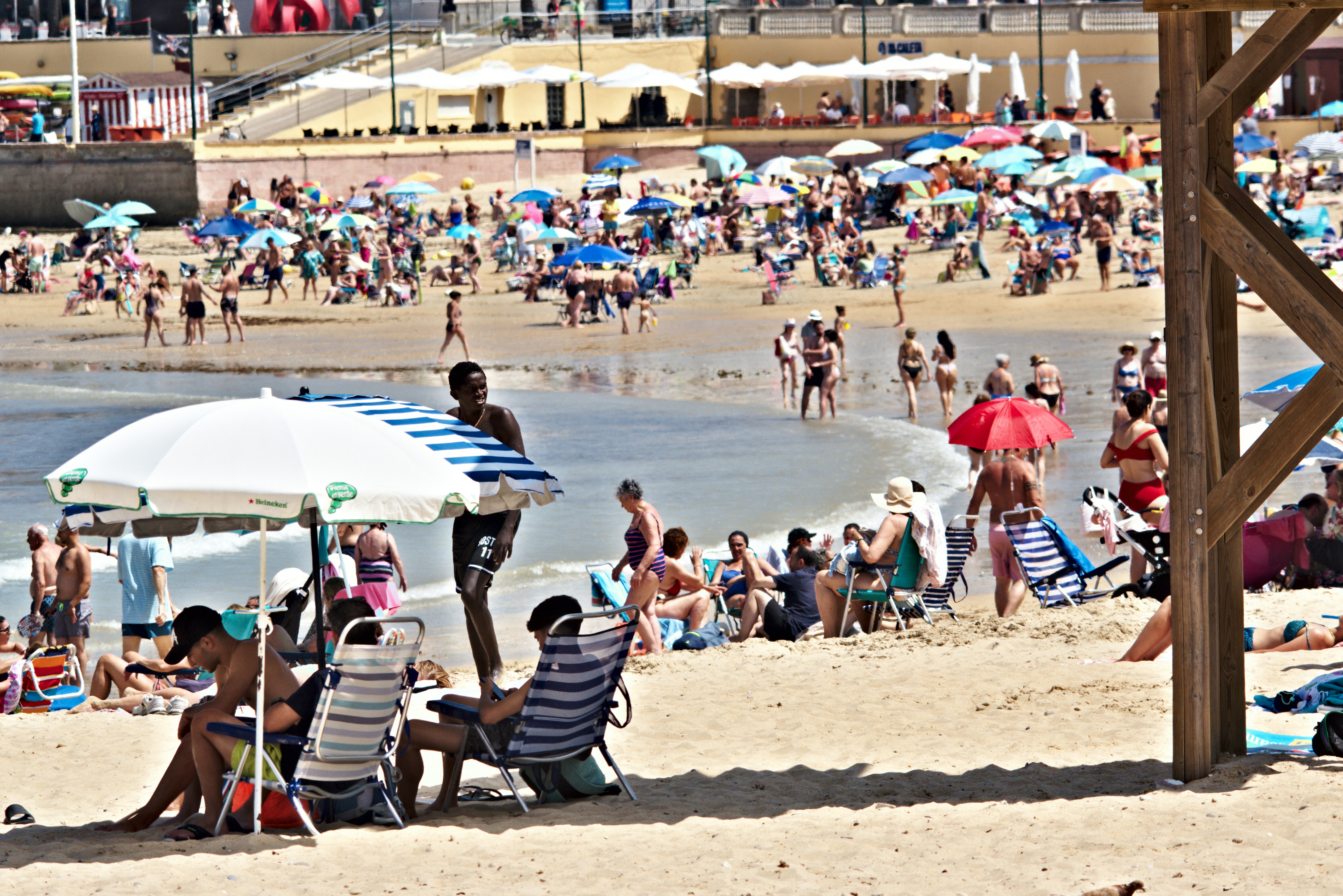Crowded beach scene with colorful umbrellas and sunbathers enjoying a sunny day by the water. The lively atmosphere captures the essence of summer leisure.