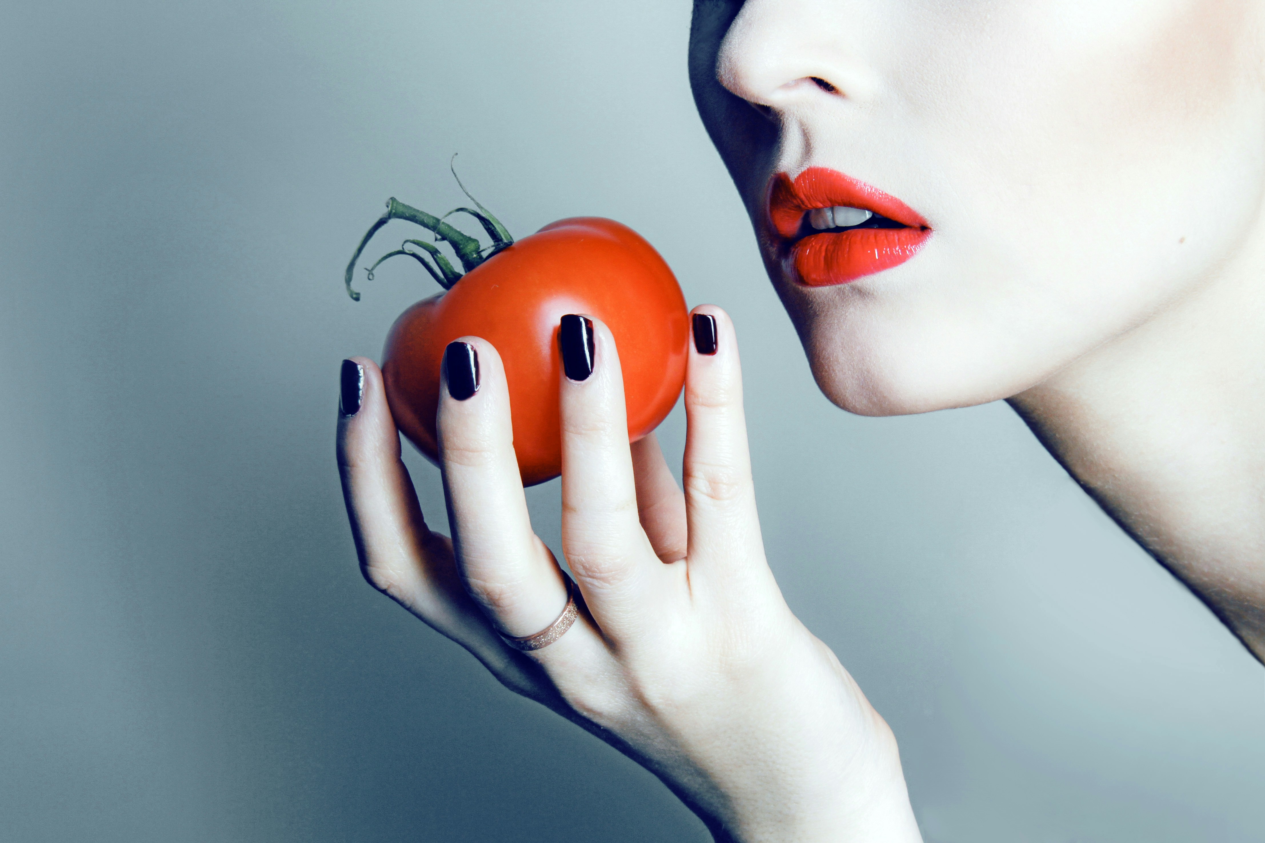 Tomato Desire – Minimal meets Pop Ein ikonisches Beauty-Food-Stillleben mit klarer Formsprache, Farbe und Kontrast. | Woman holds a tomato, ready to eat.