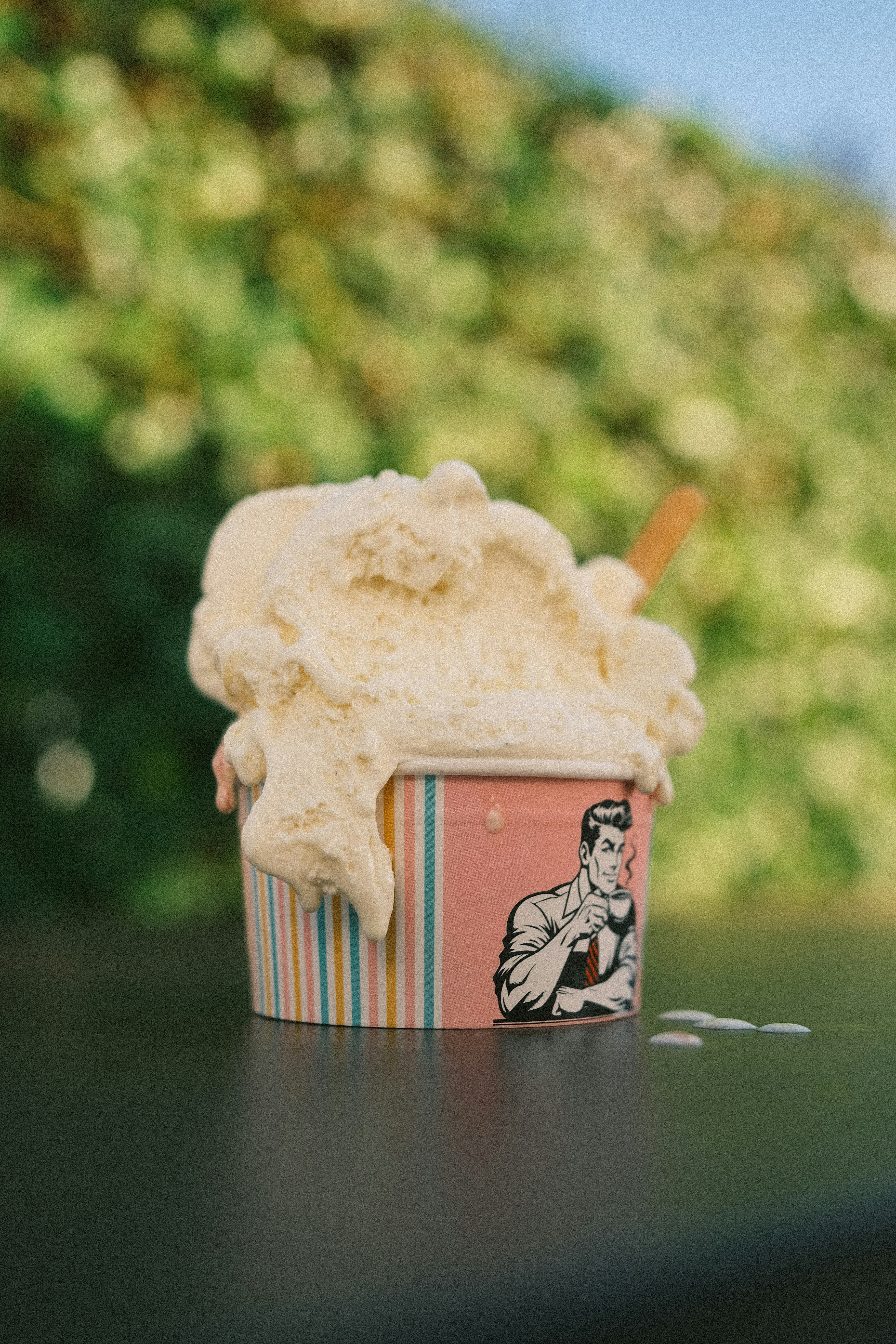 Cup of creamy vanilla ice cream topped with a wooden spoon, featuring a vintage comic character on its side. 