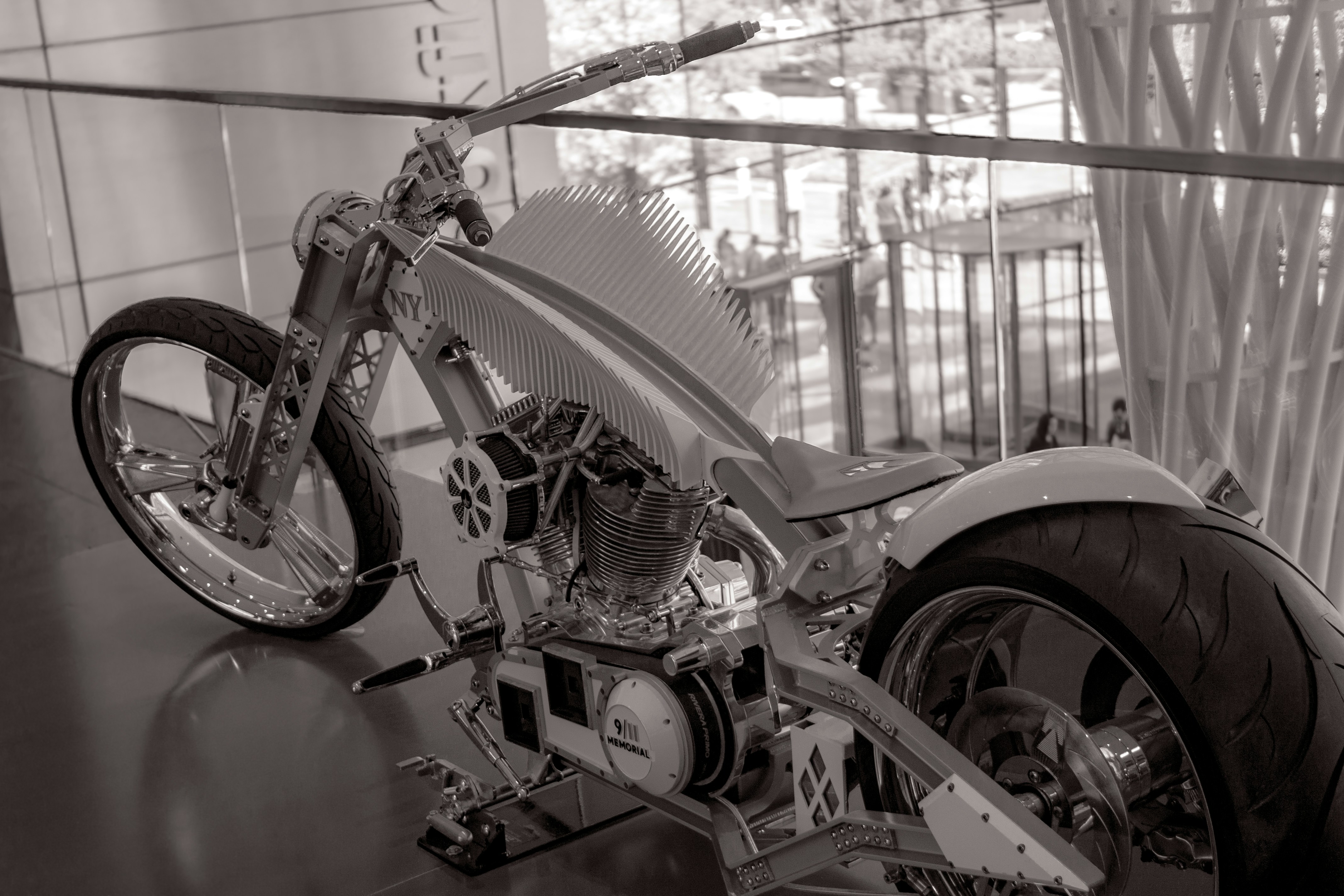 A sleek, modern motorcycle with an innovative design featuring a prominent rear wheel and distinctive bodywork. The setting showcases a contemporary architectural backdrop.