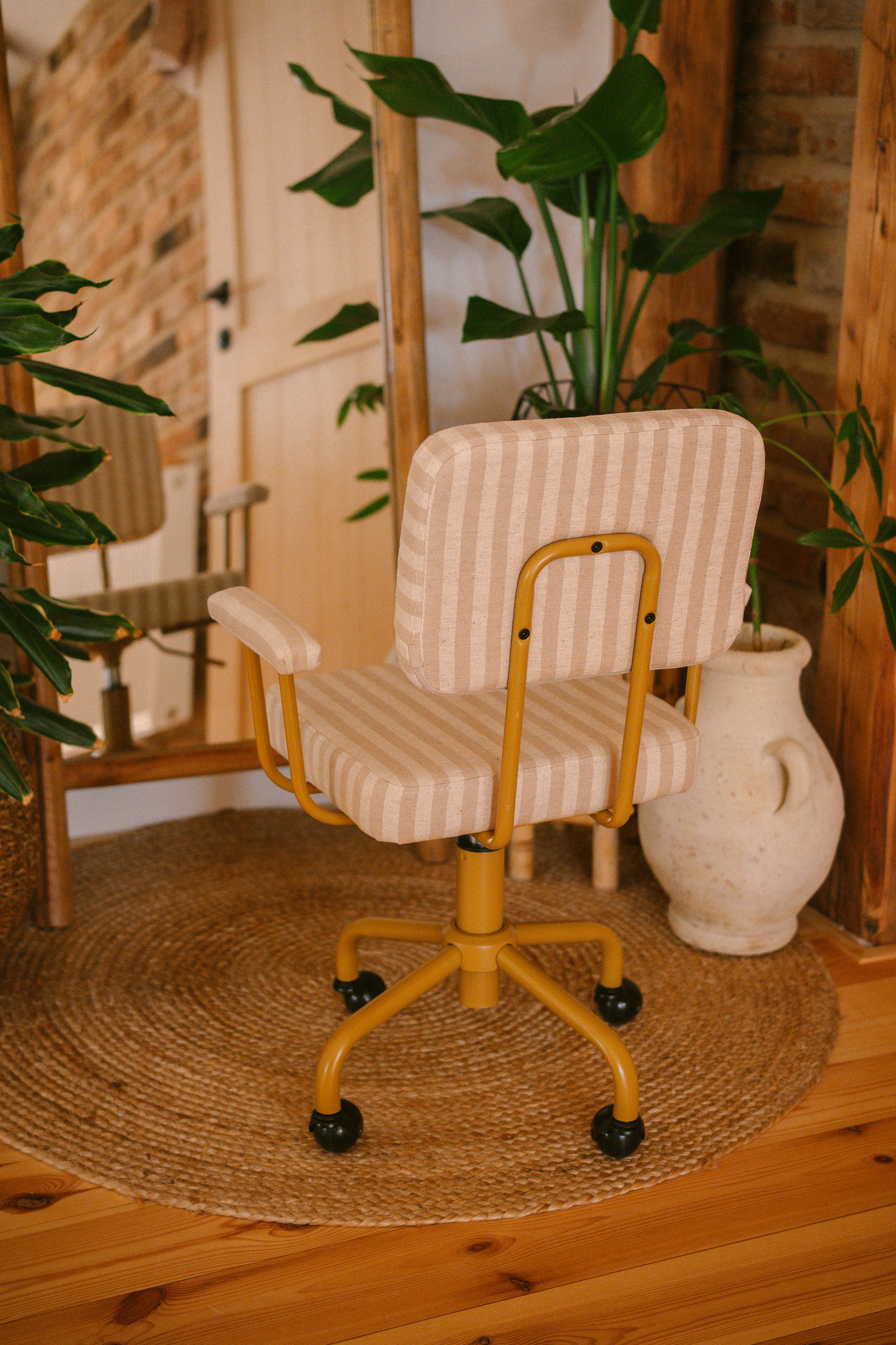 Retro office chair with striped upholstery positioned near a mirror and surrounded by greenery. The warm tones and textures create a welcoming atmosphere.