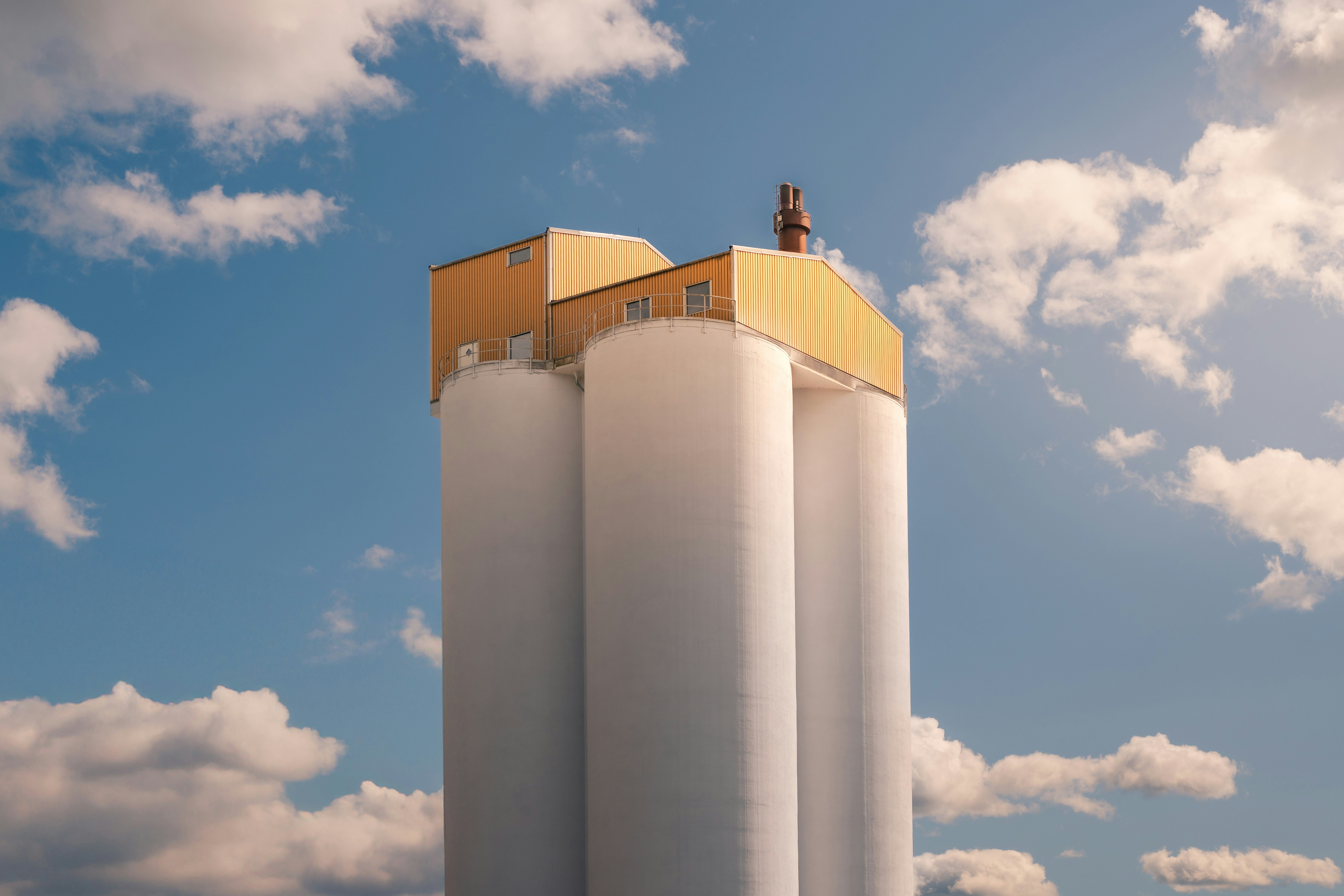 House on the Silos. A remarkable architectural feature in Kongsvinger, Norway, where a bright yellow, house-like structure sits atop a set of towering white silos. | Tall industrial silos reaching towards the sky.