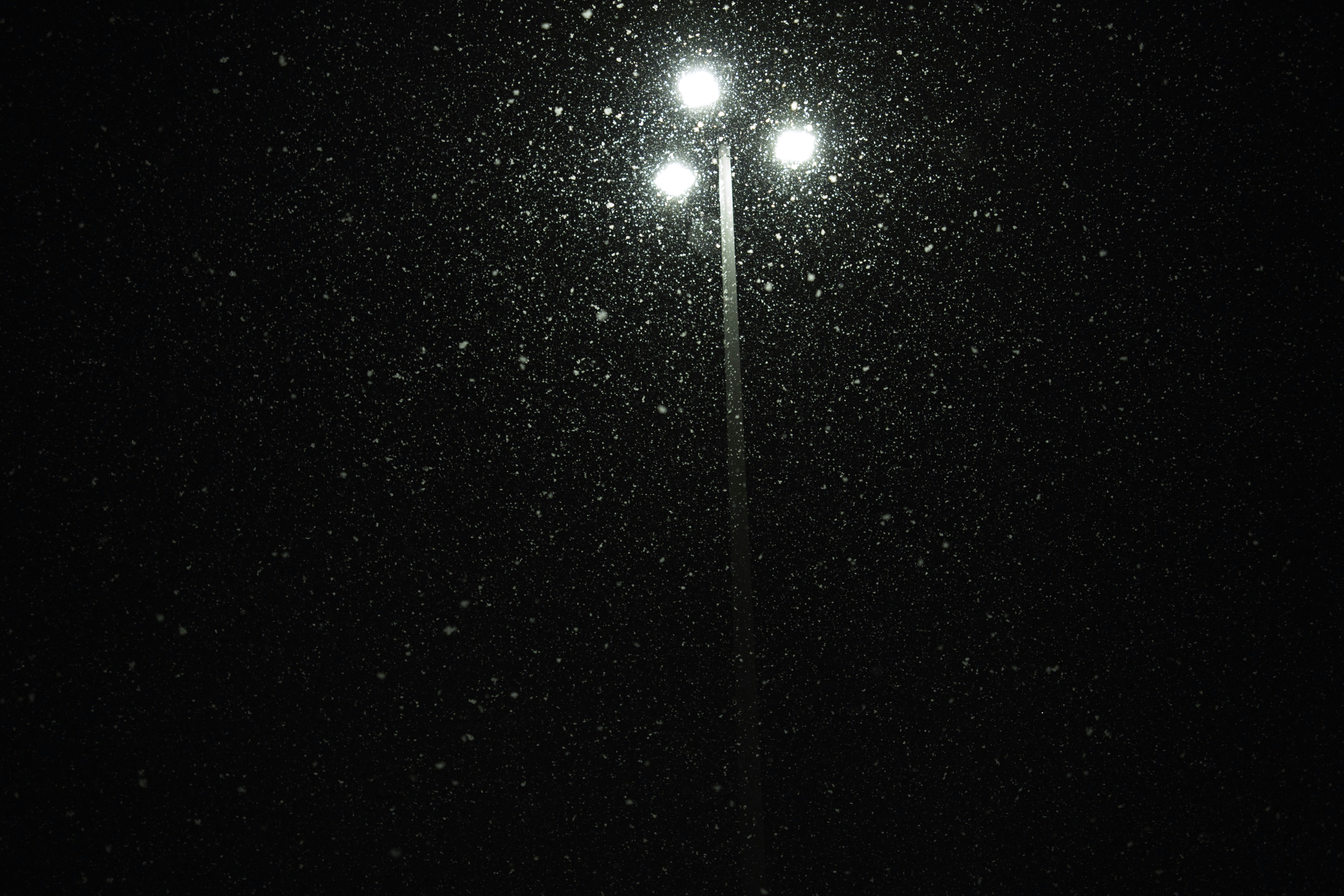 A streetlight casts a glowing halo amidst swirling snowflakes in the darkness. The scene evokes a serene winter atmosphere.