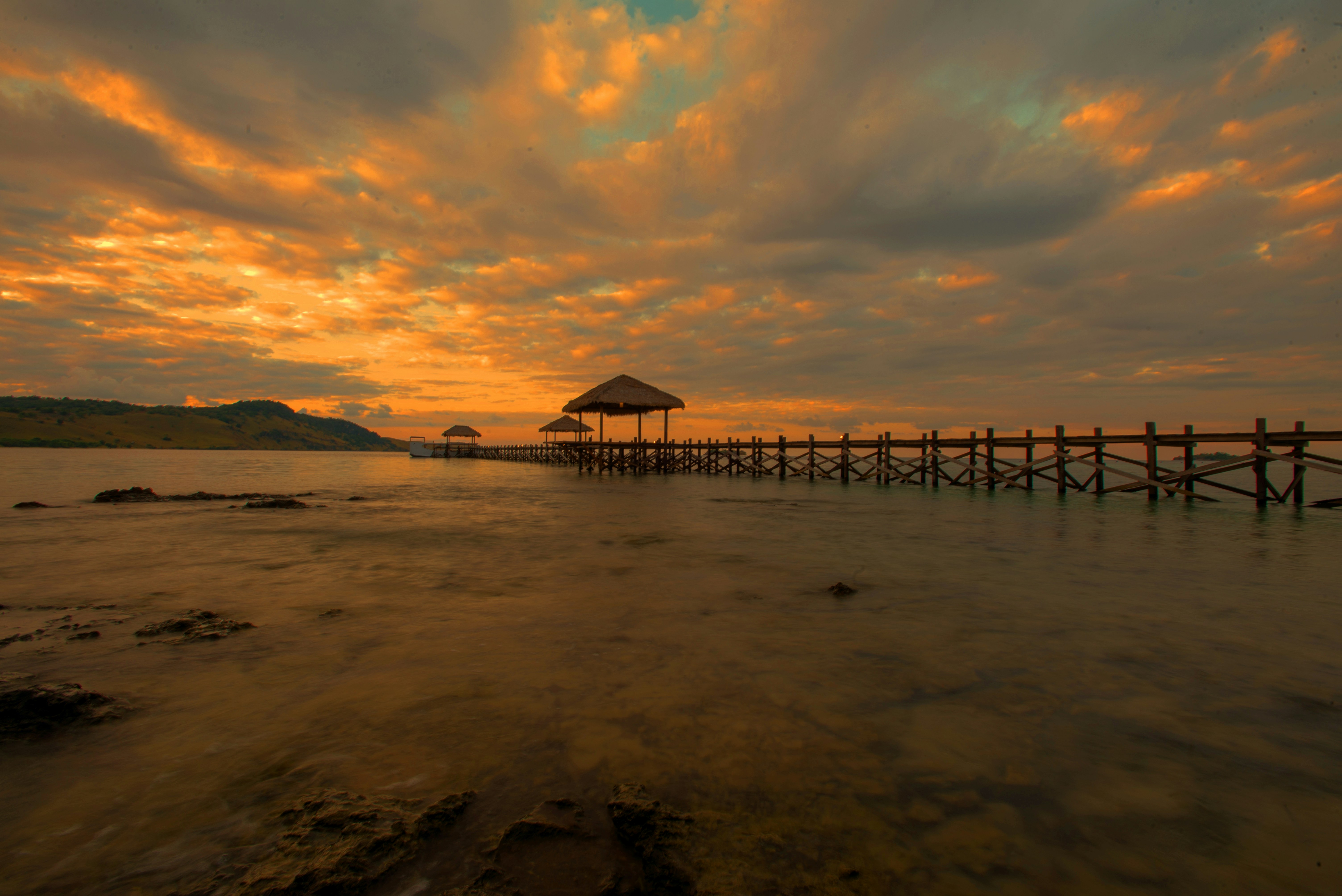 Wooden pier extending into a serene body of water under a dramatic sky at sunset.