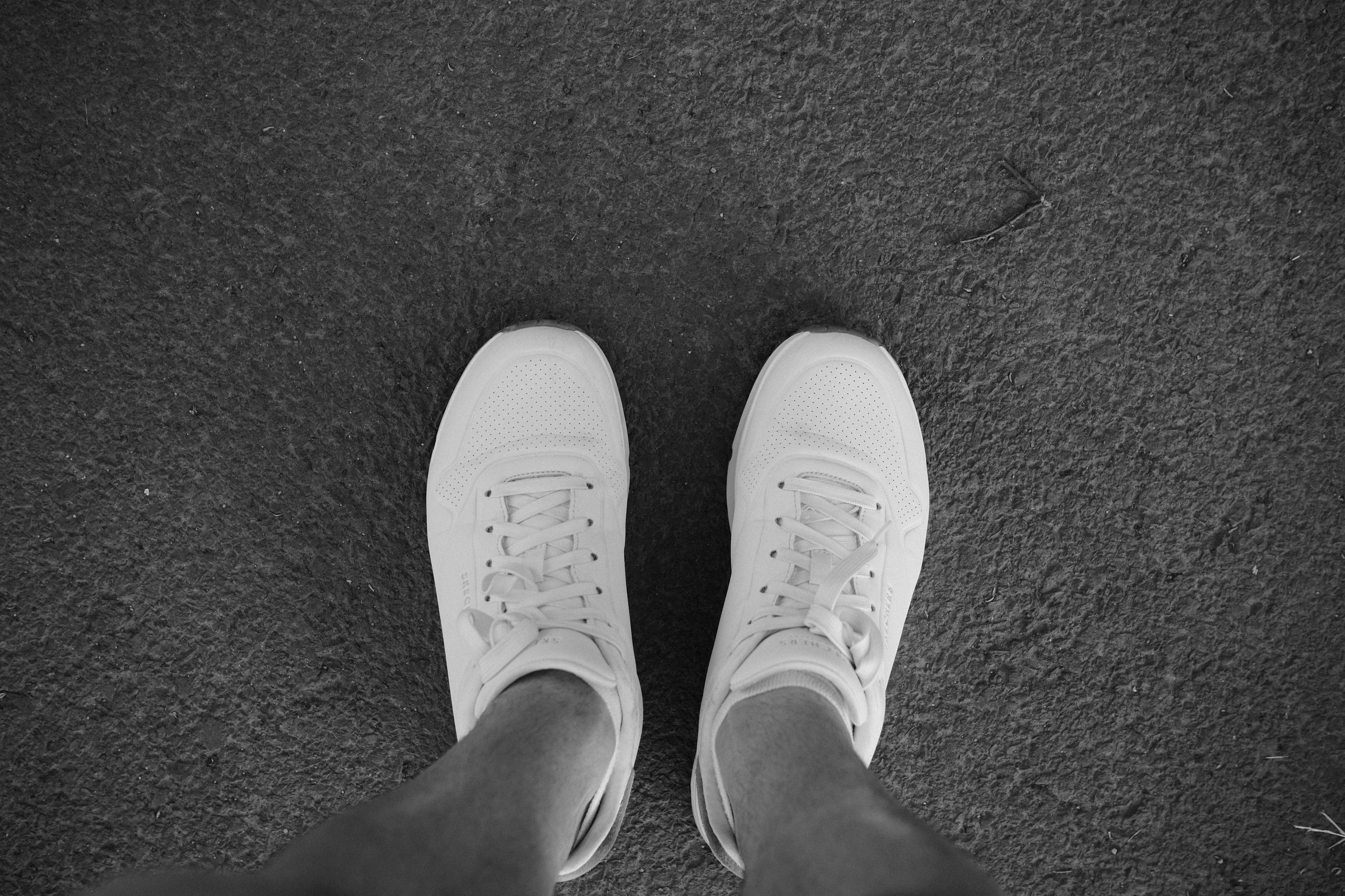 White athletic shoes on pavement in urban area | White sneakers standing on textured ground.