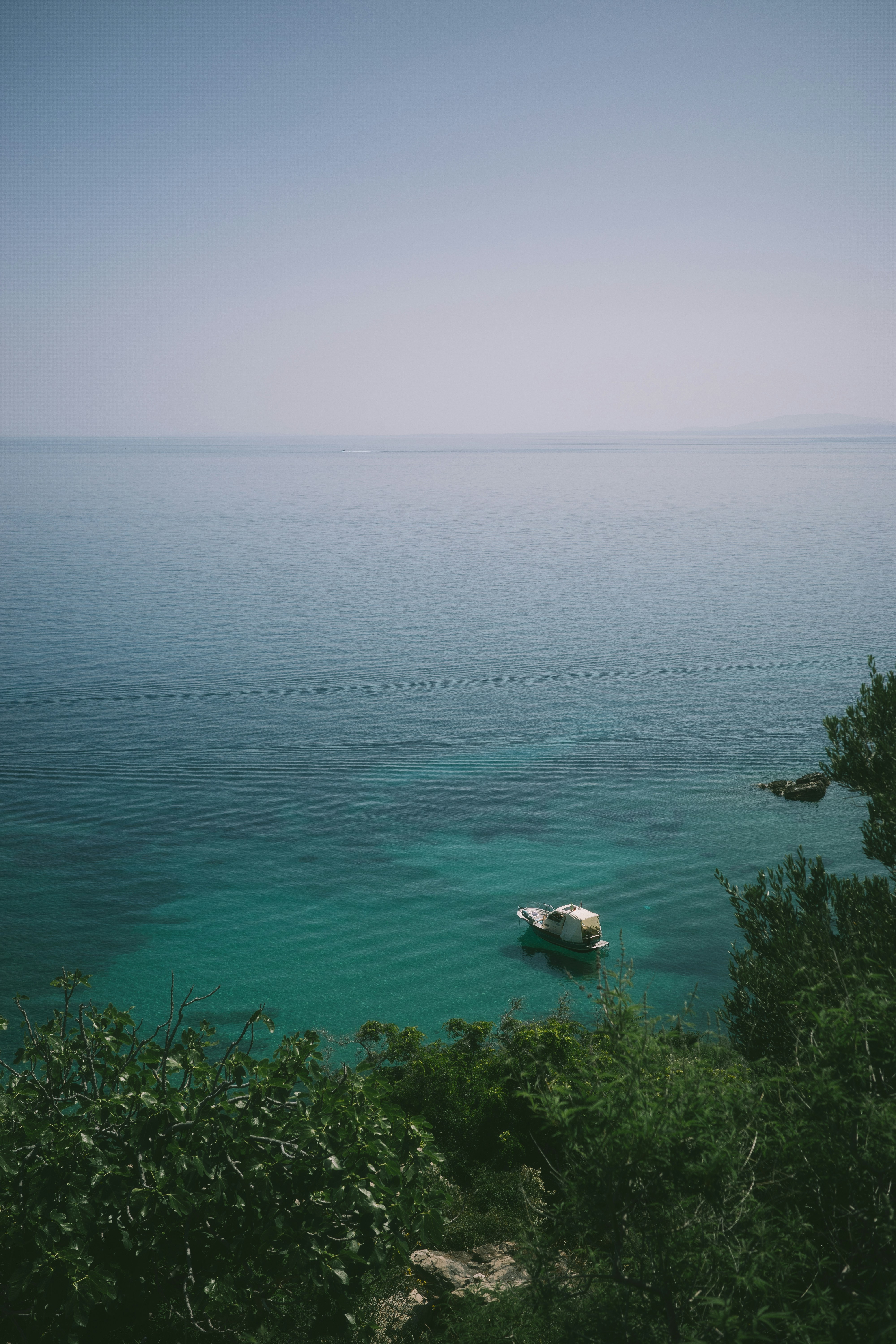 A tranquil scene featuring a small boat anchored in calm, turquoise waters, framed by lush greenery along the shoreline.