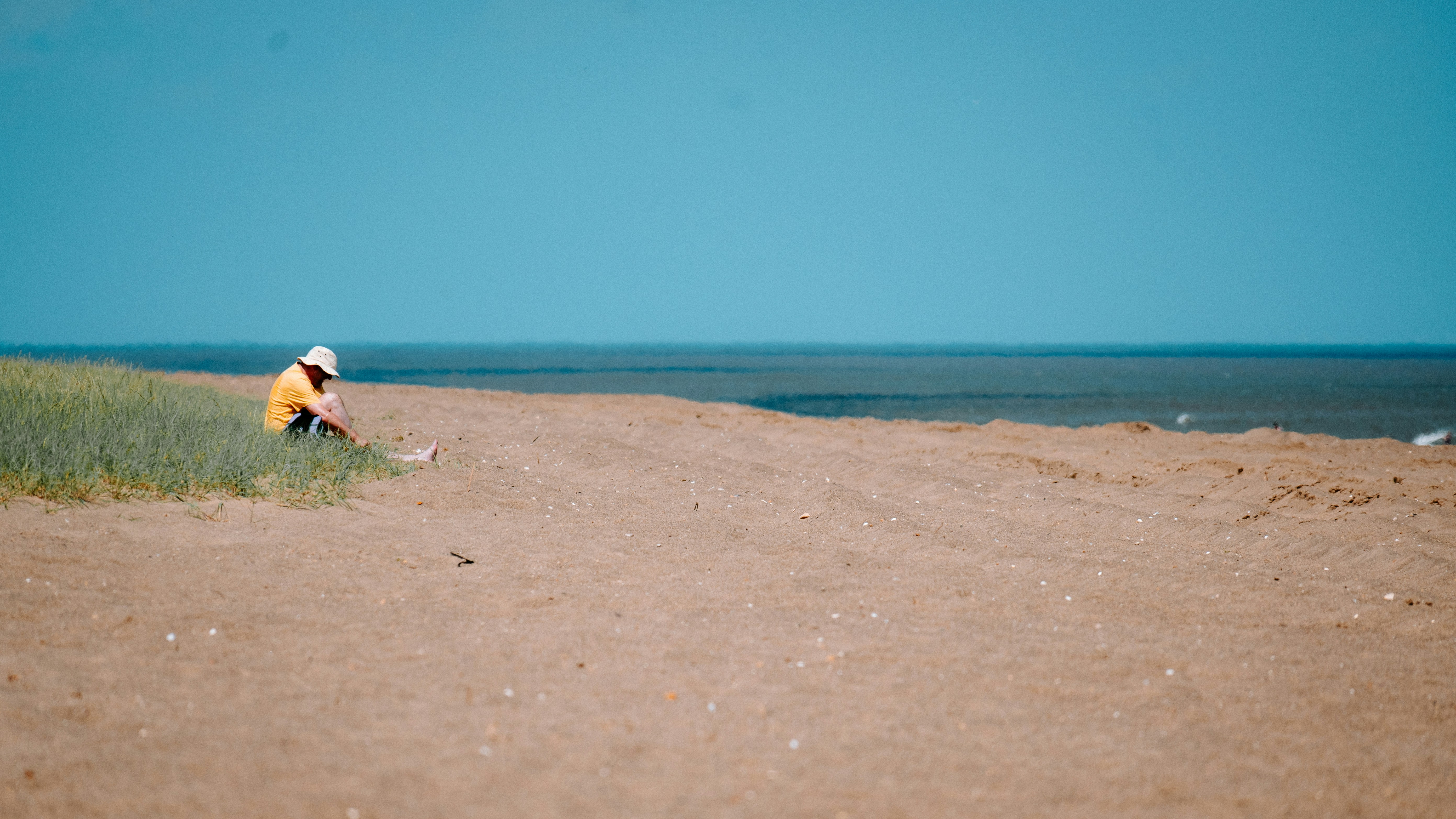 Individual seated on a sandy beach, engaged in a quiet moment of reflection with a vast ocean backdrop.
