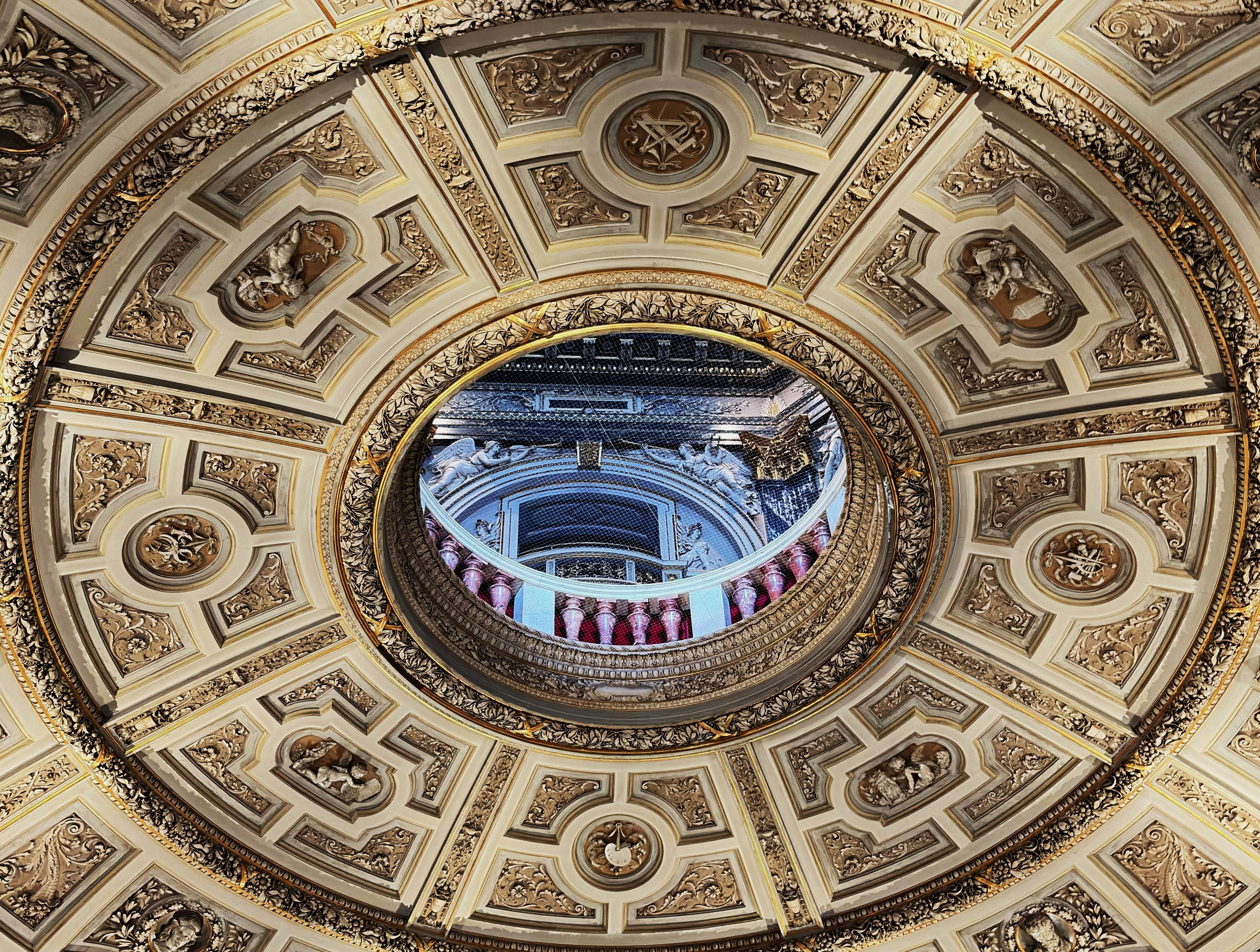 Intricate ceiling design showcasing elaborate carvings and a central opening revealing a glimpse of the grand architecture above.