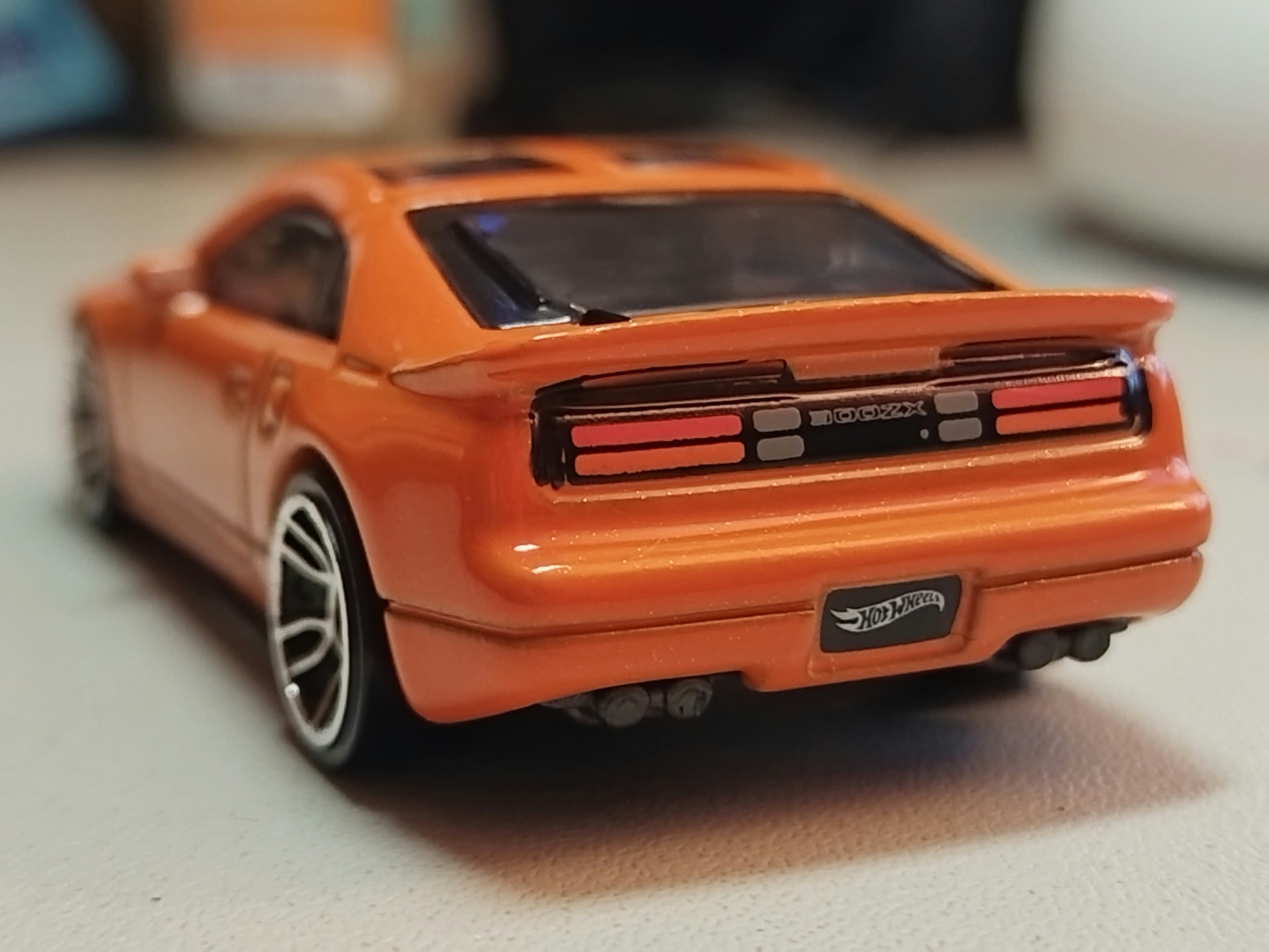 Detailed close-up of a vibrant orange toy car, showcasing its sleek design and intricate features. The focus highlights the rear view with distinctive taillights.
