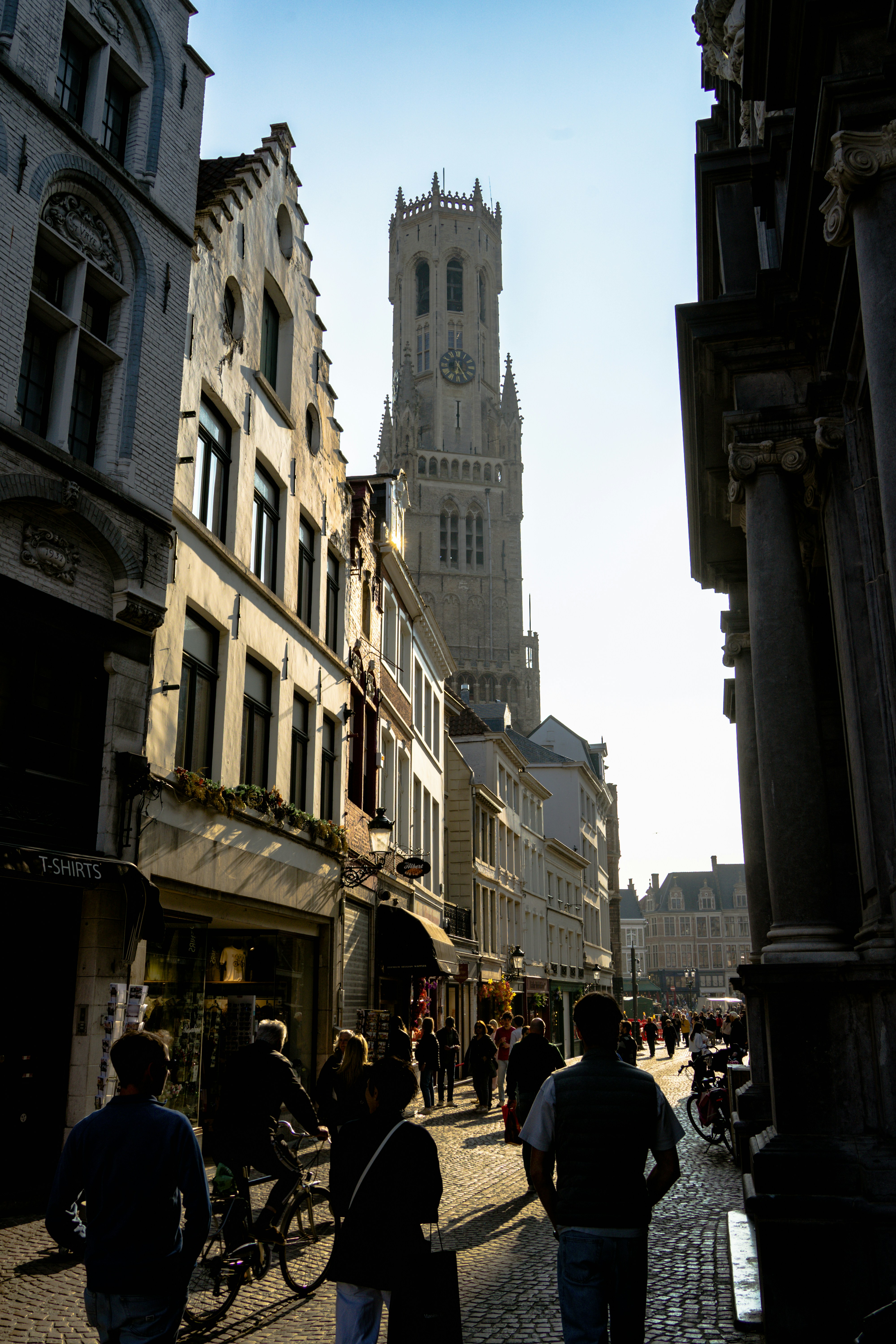 Historic street bustling with pedestrians, framed by charming architecture and the towering clock tower in the background. 