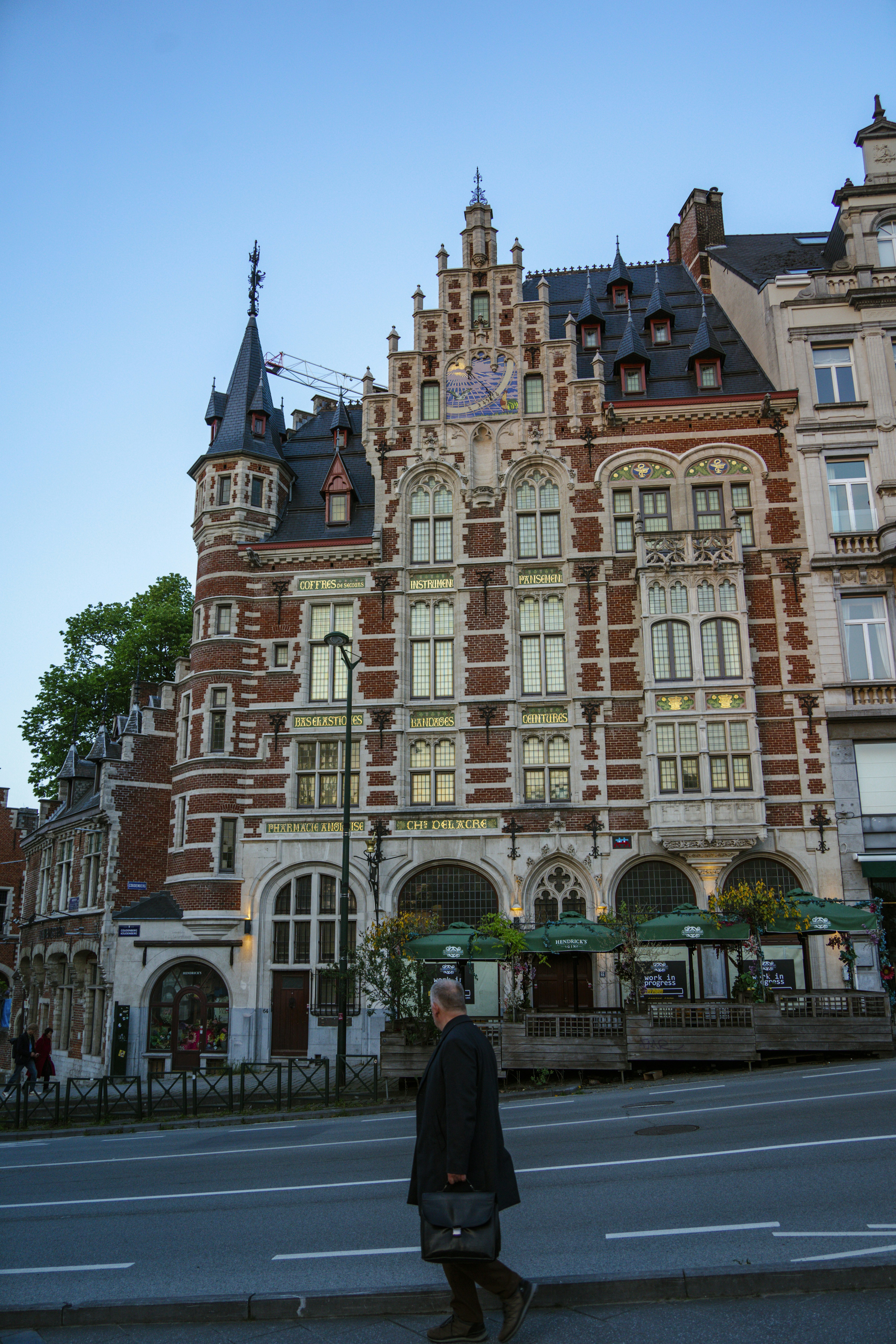 Historic building with intricate brickwork and ornate details, featuring a man walking past. The scene captures urban life against a backdrop of architectural beauty.