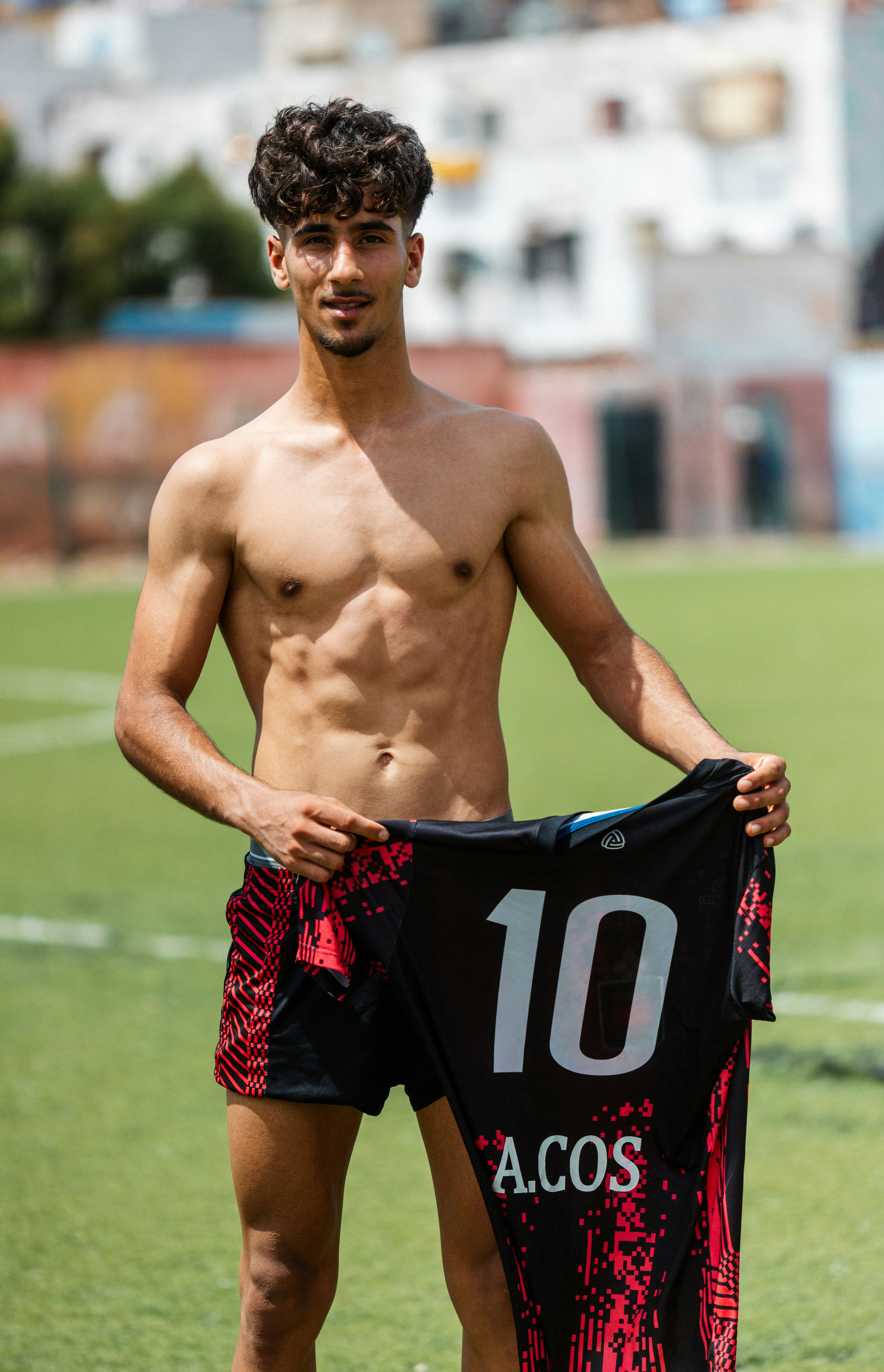A young athlete proudly holds up his jersey on a vibrant soccer field, showcasing his dedication to the sport. The background hints at a lively community atmosphere.