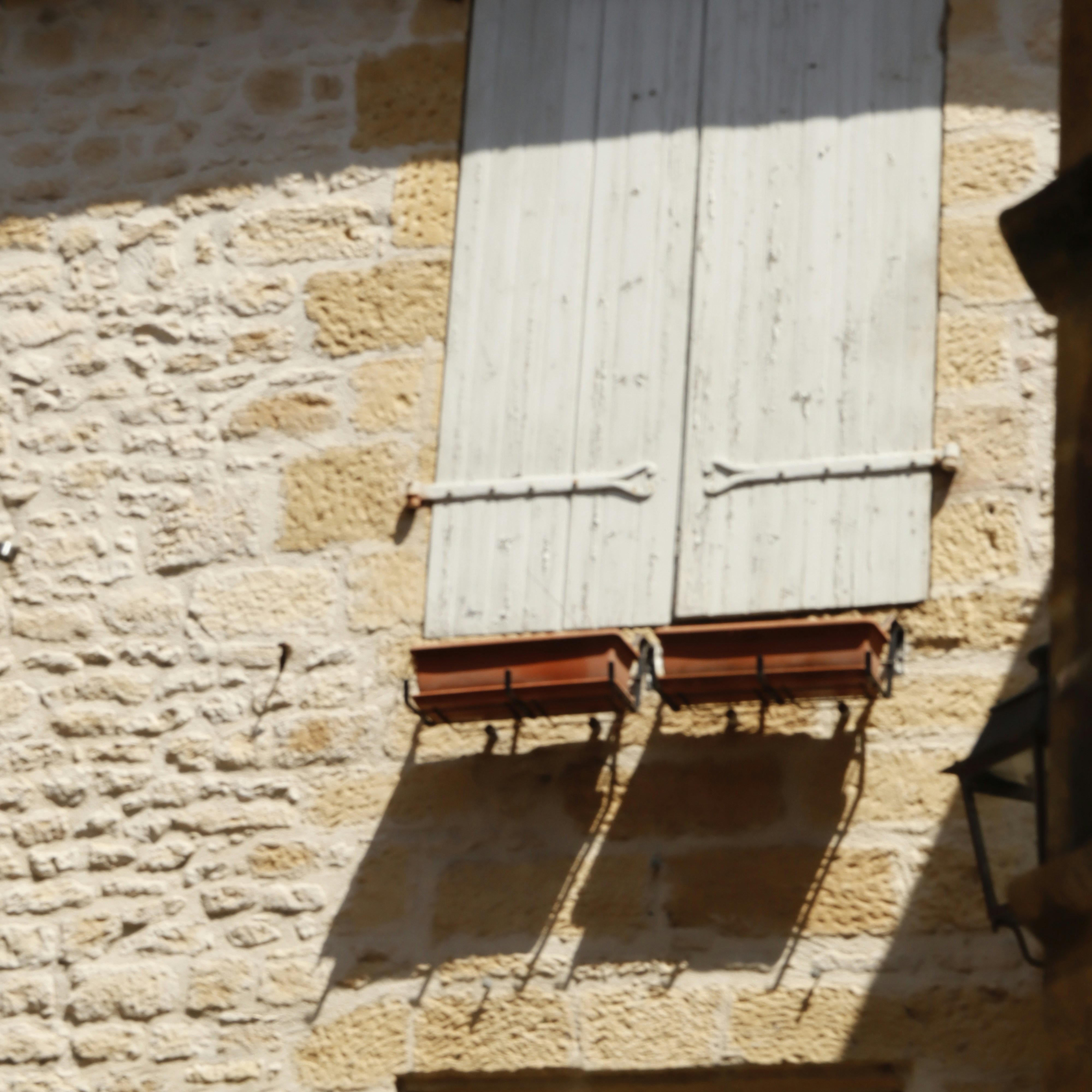 Weathered wooden shutters adorned with flower boxes against a textured stone wall, evoking a sense of vintage tranquility.