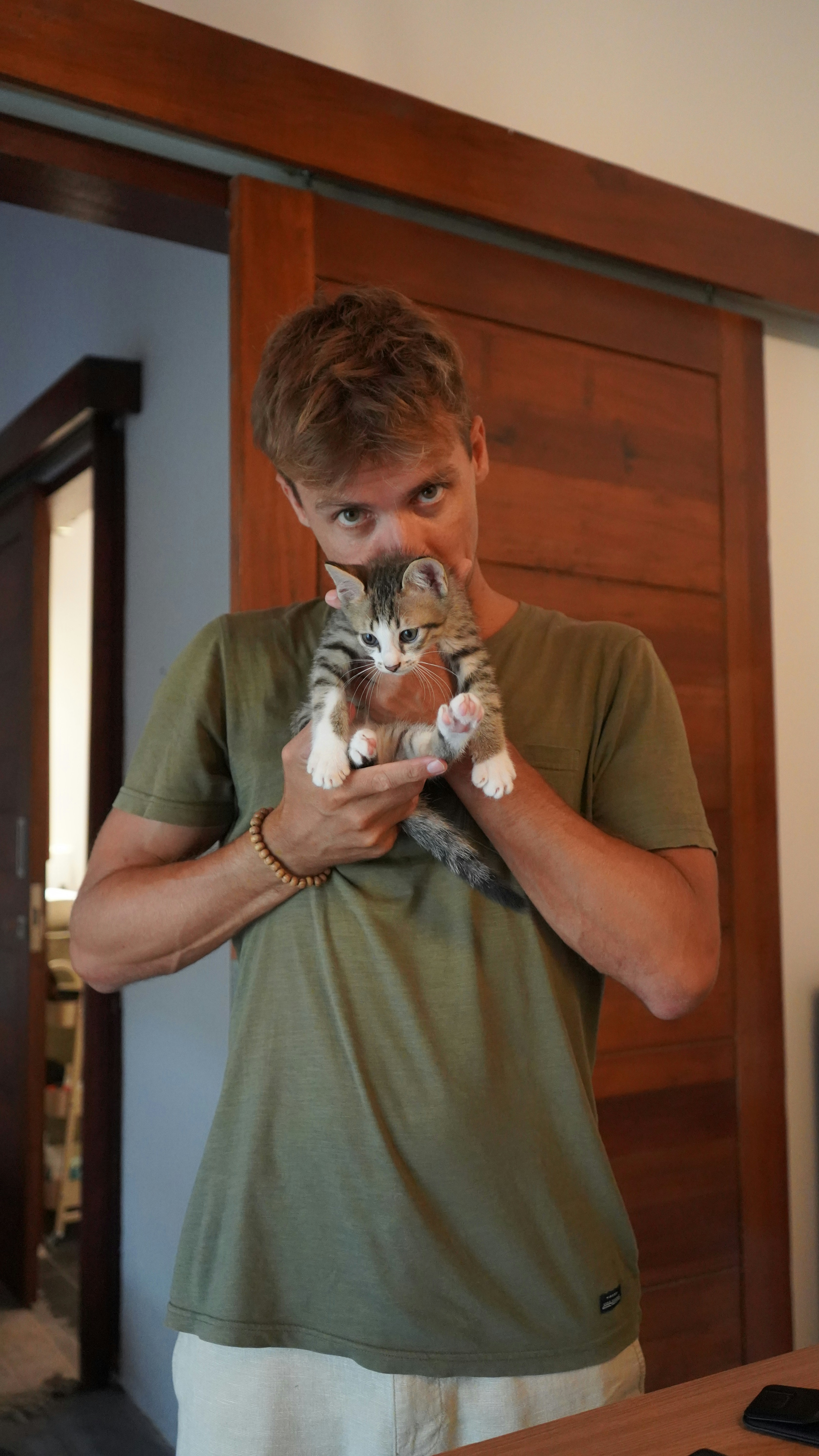 A man gently holds an adorable kitten close in a warm indoor scene. | A man holds a cute kitten.