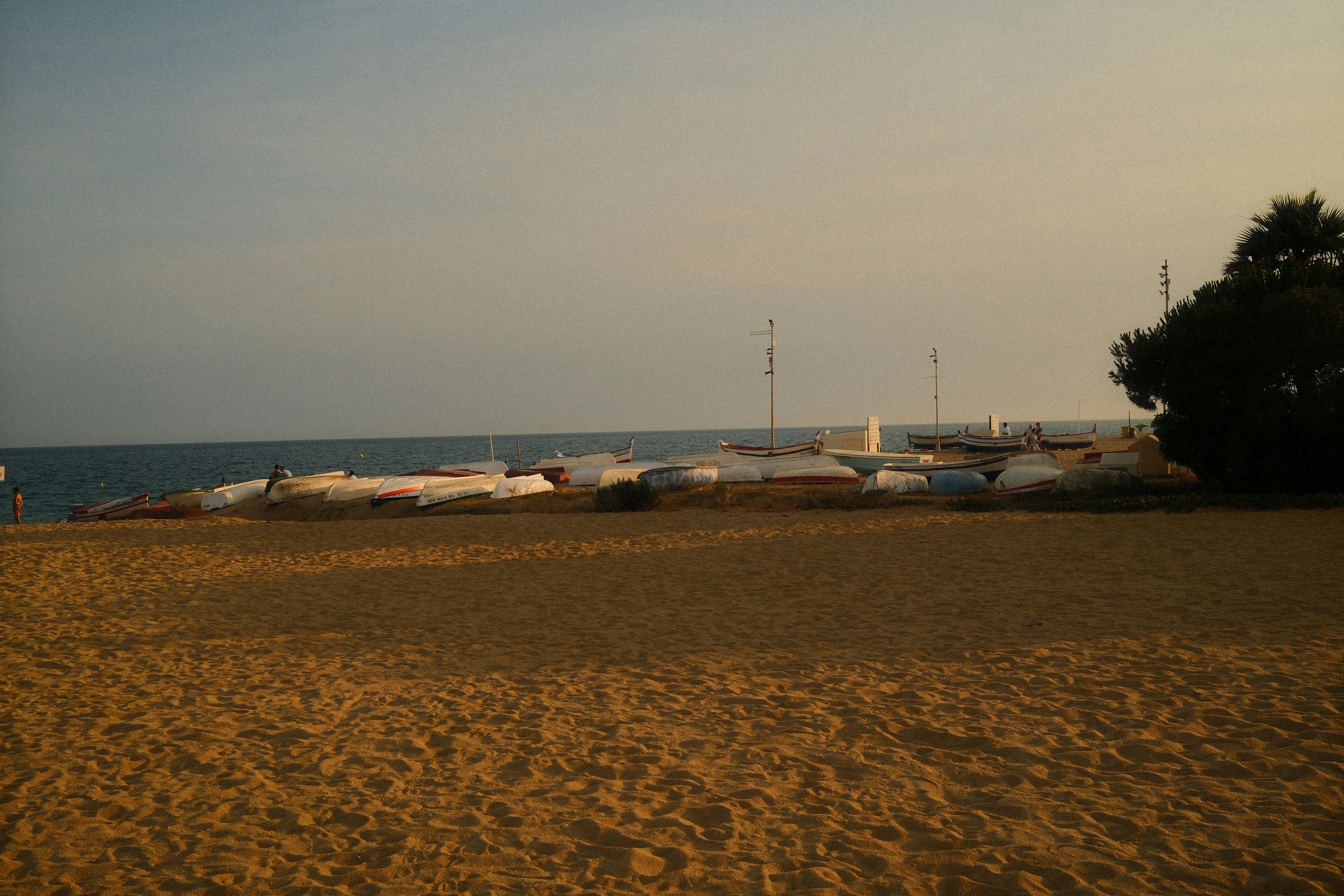 Boats rest on a sandy shore near the ocean.