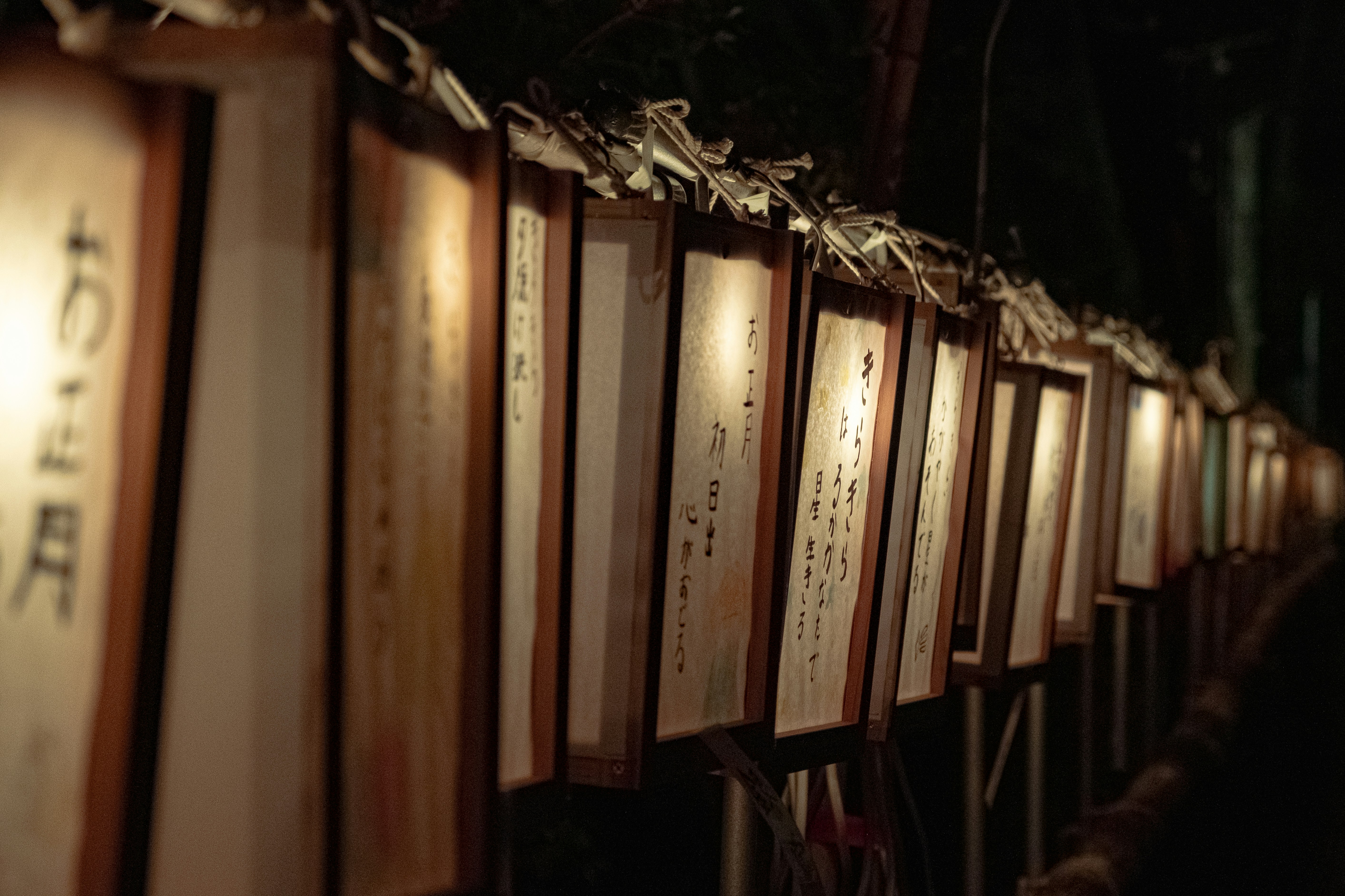A row of softly glowing lanterns adorned with calligraphy, casting a warm light in a serene nighttime setting.
