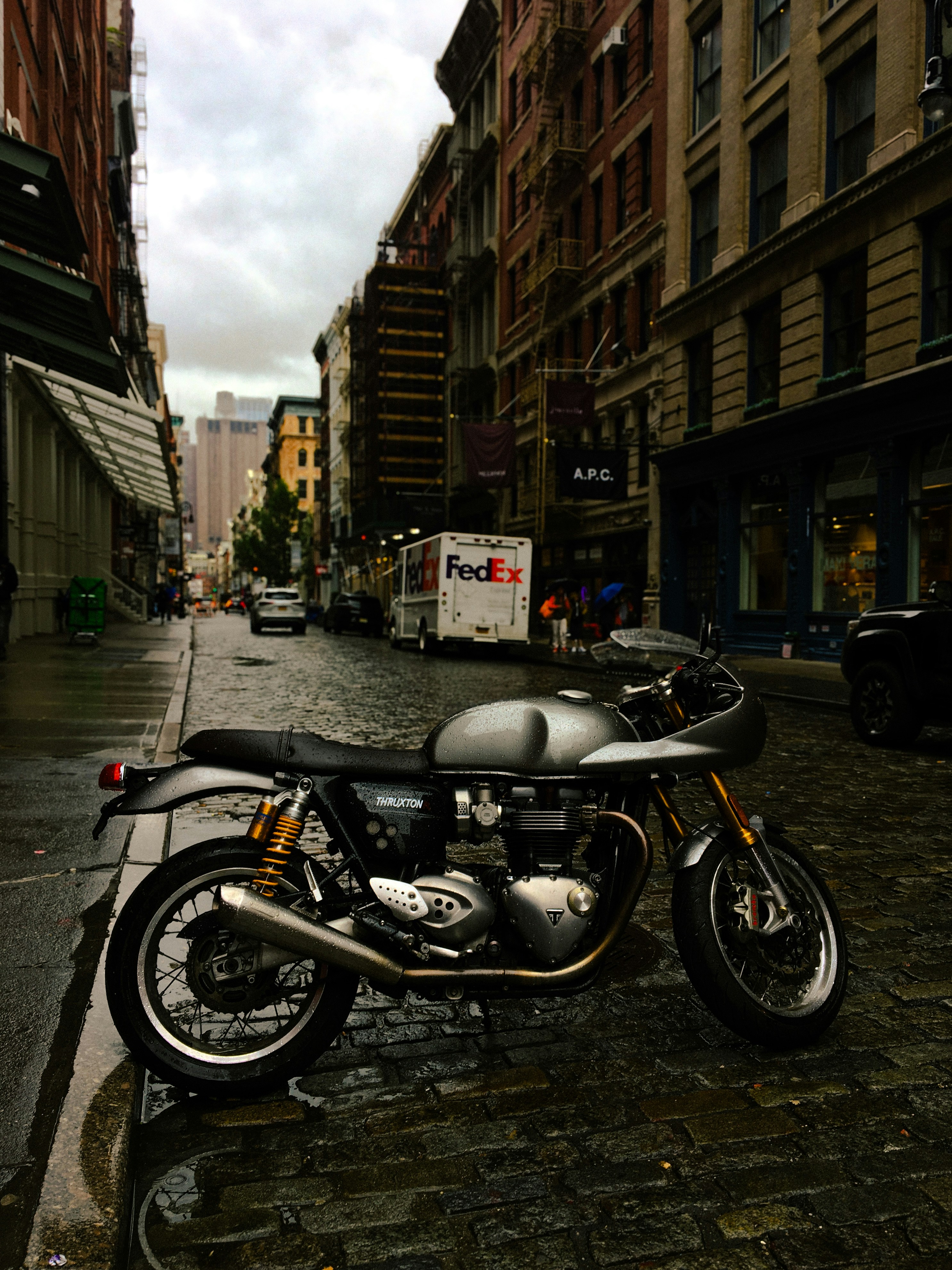 Classic motorcycle parked on a cobblestone street, surrounded by historic buildings and a moody sky.