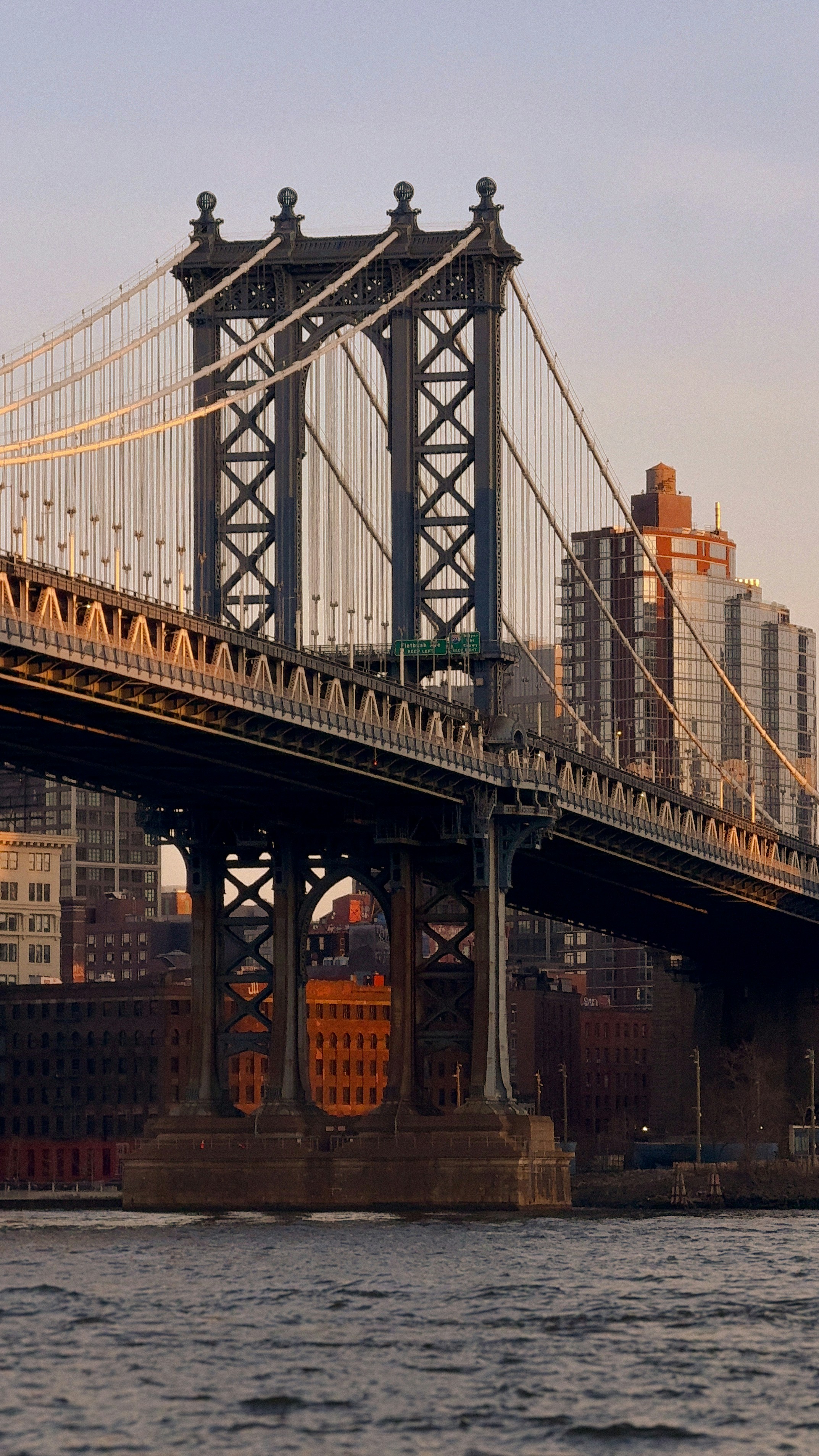 The manhattan bridge is seen over the water.