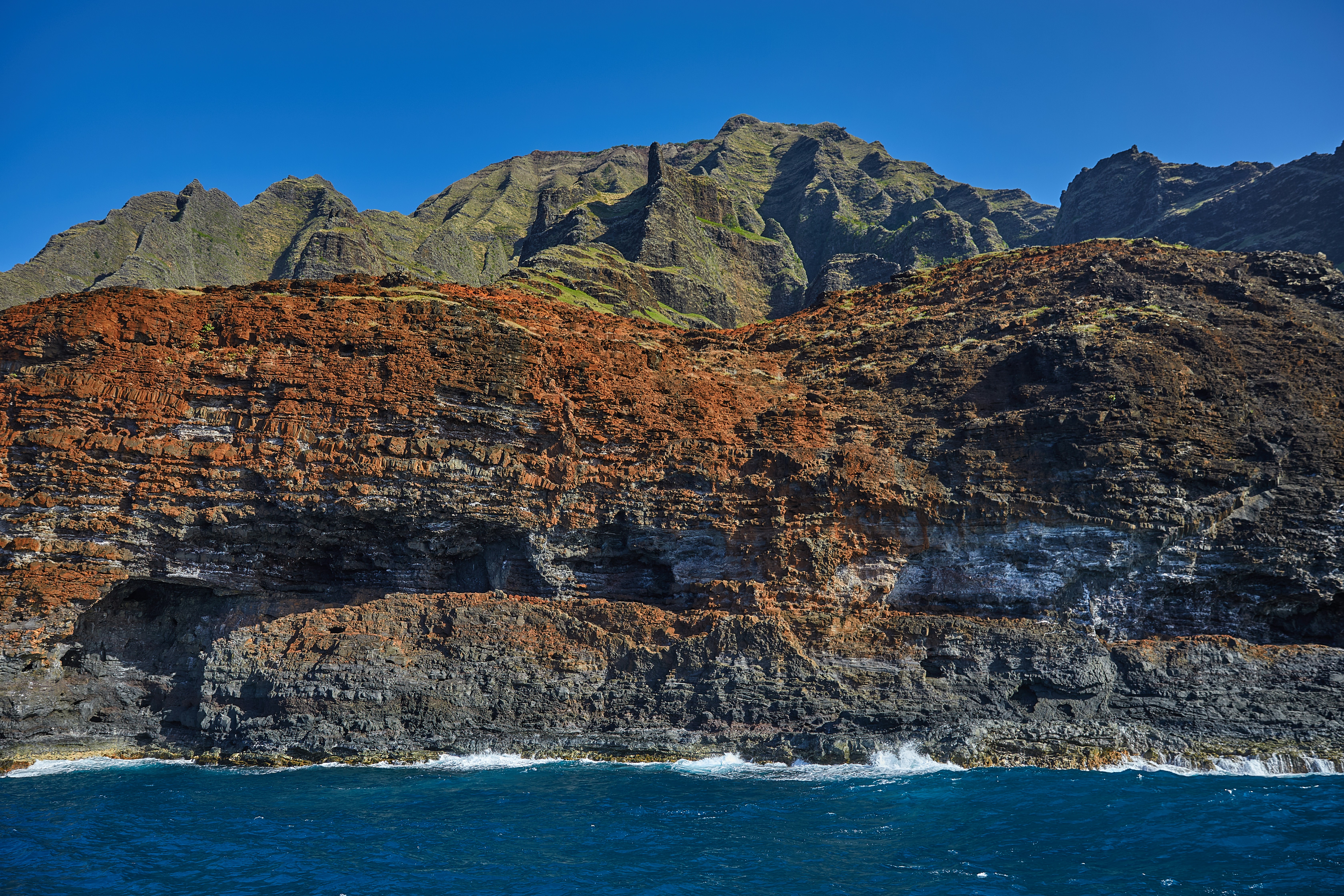 Vivid red and dark rocky cliffs rise sharply from the turquoise sea, showcasing the rugged beauty of coastal geology.