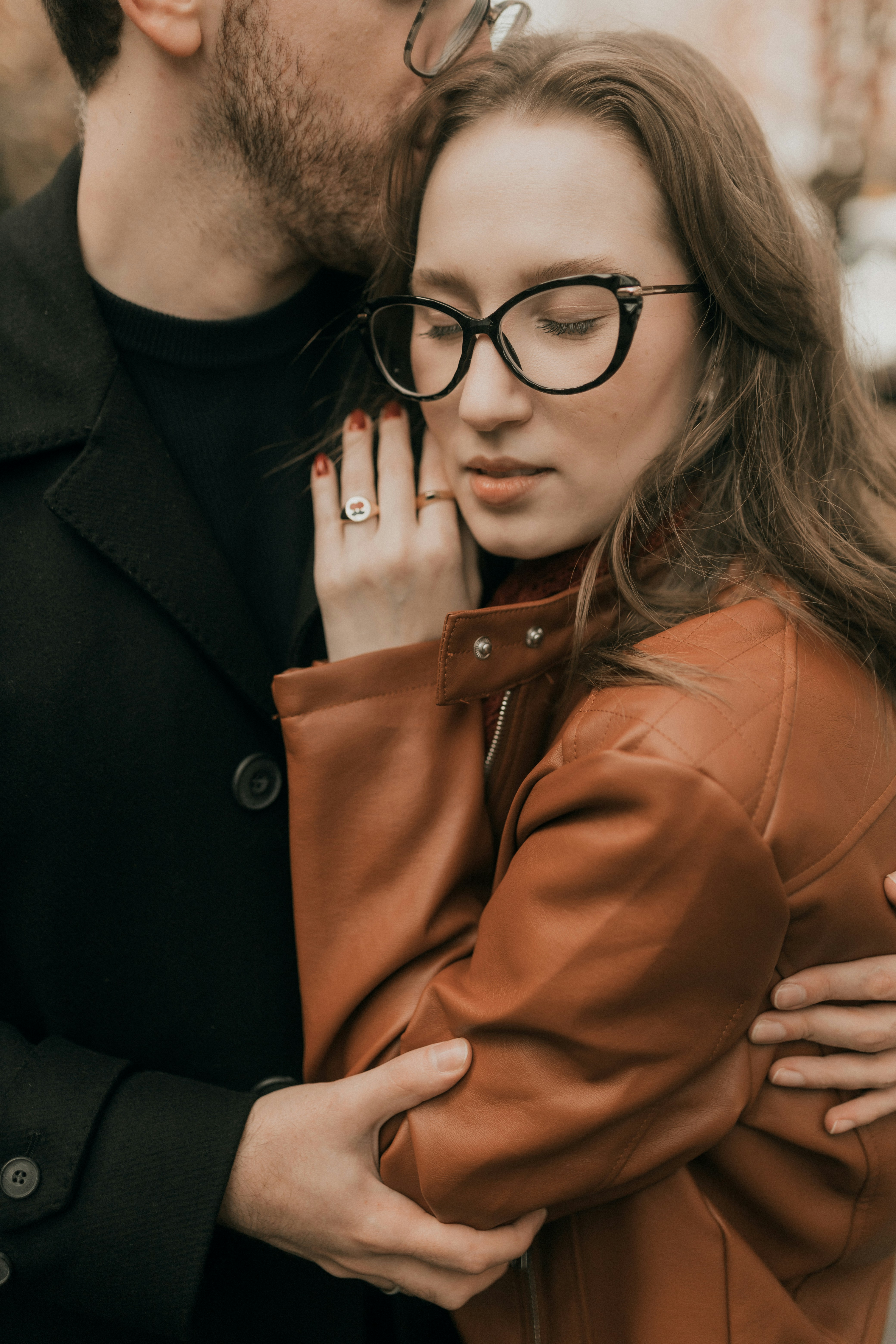 A couple sharing a tender moment, with the woman in a brown leather jacket and the man in a black coat, conveying warmth and intimacy.