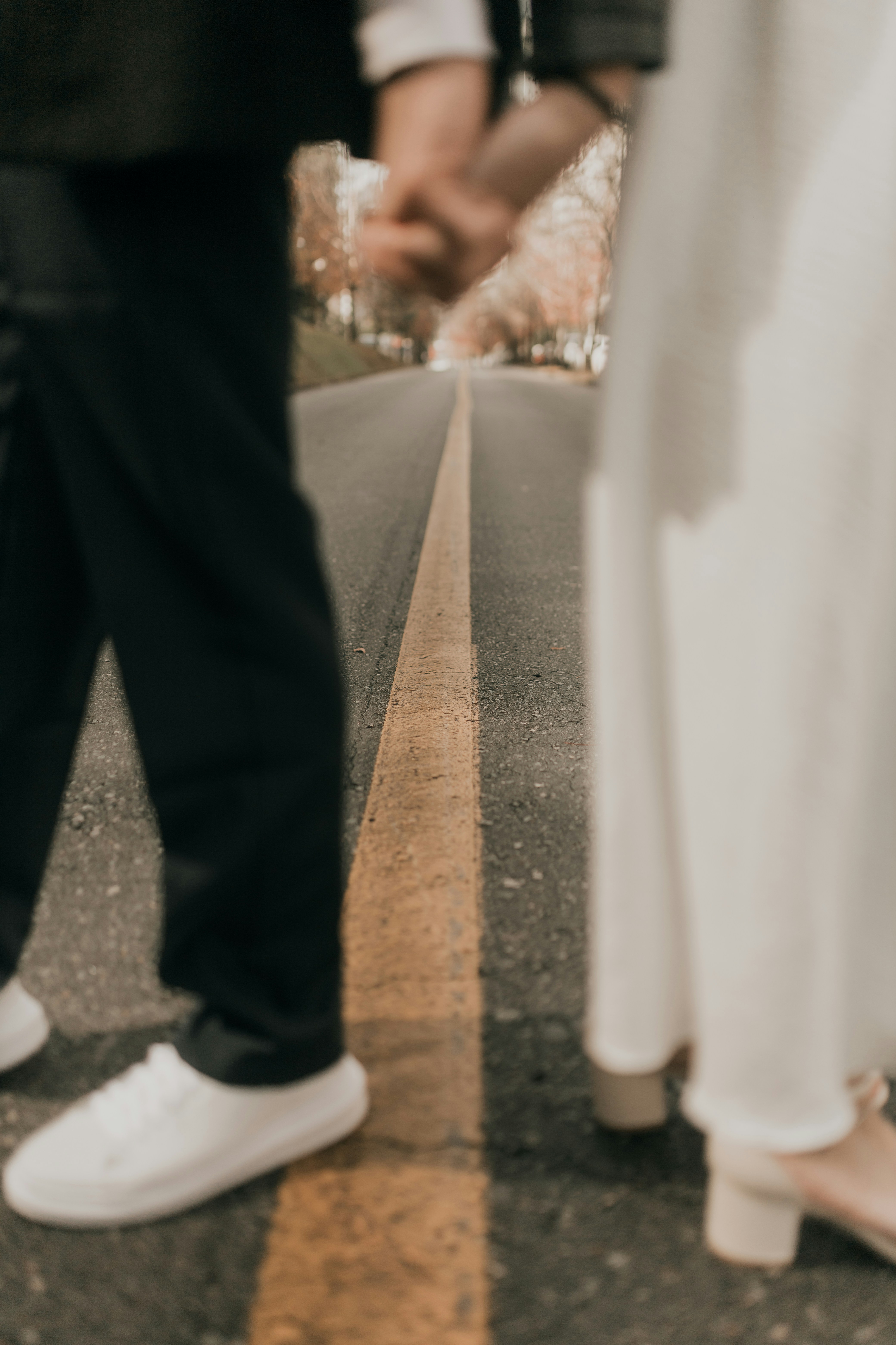 Couple holding hands, standing on a road with a yellow center line, symbolizing unity and shared direction.